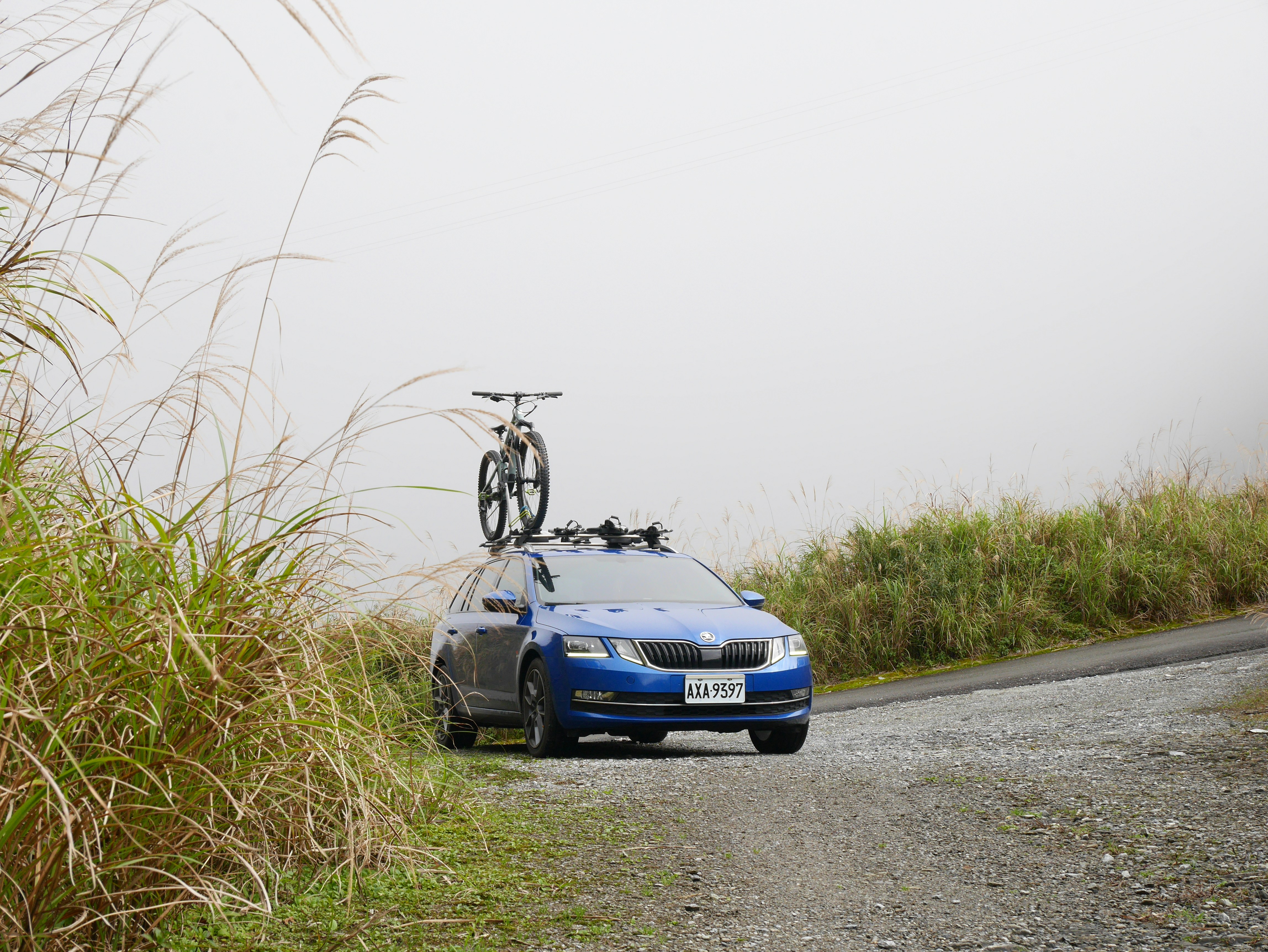 Blue car with bicycle on roof rack in foggy landscape