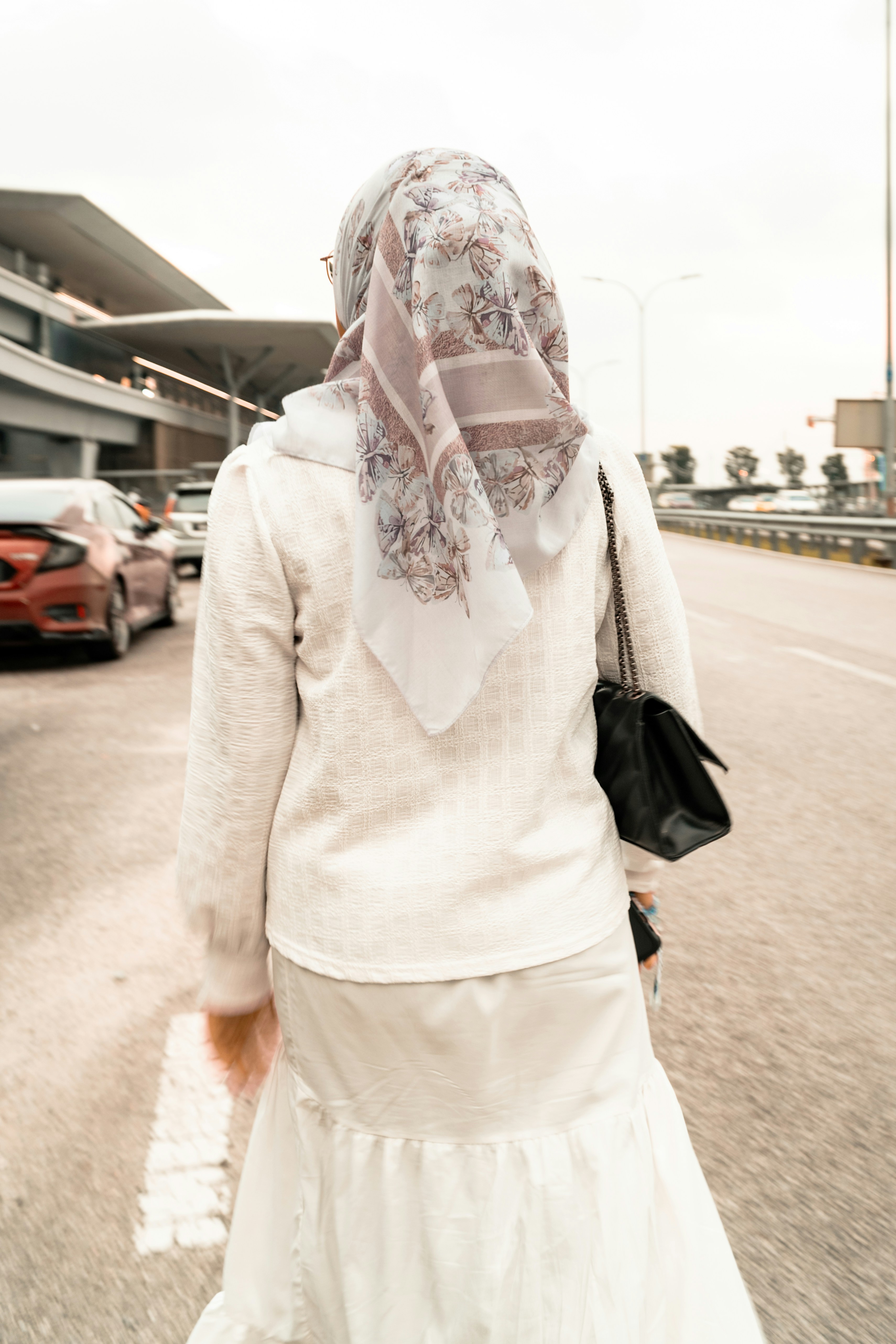 Back View in a Dusty Avenue: A Woman in a Floral Headscarf Walks Away