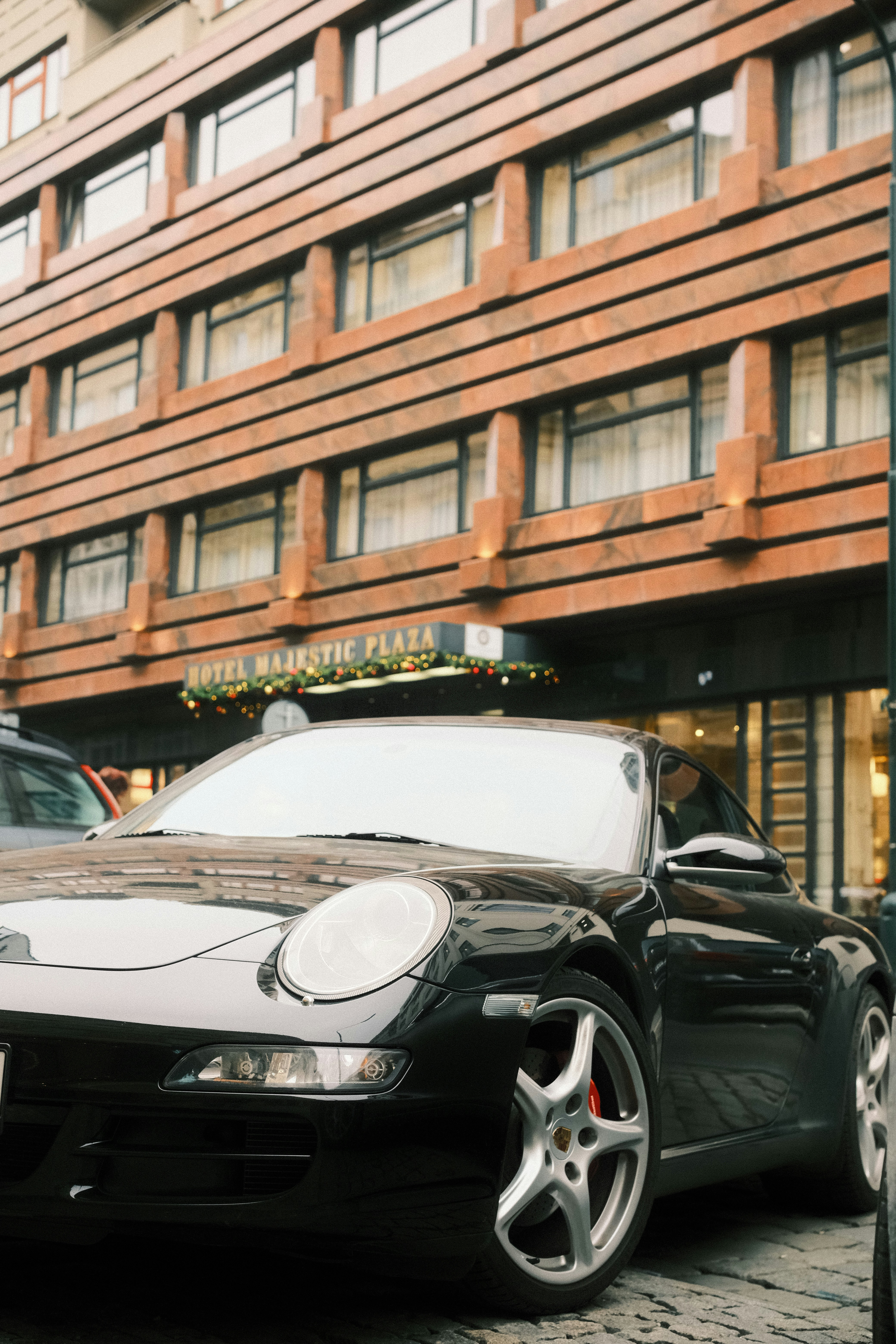 Low-angle view of a sleek black sports car parked before a brick hotel façade
