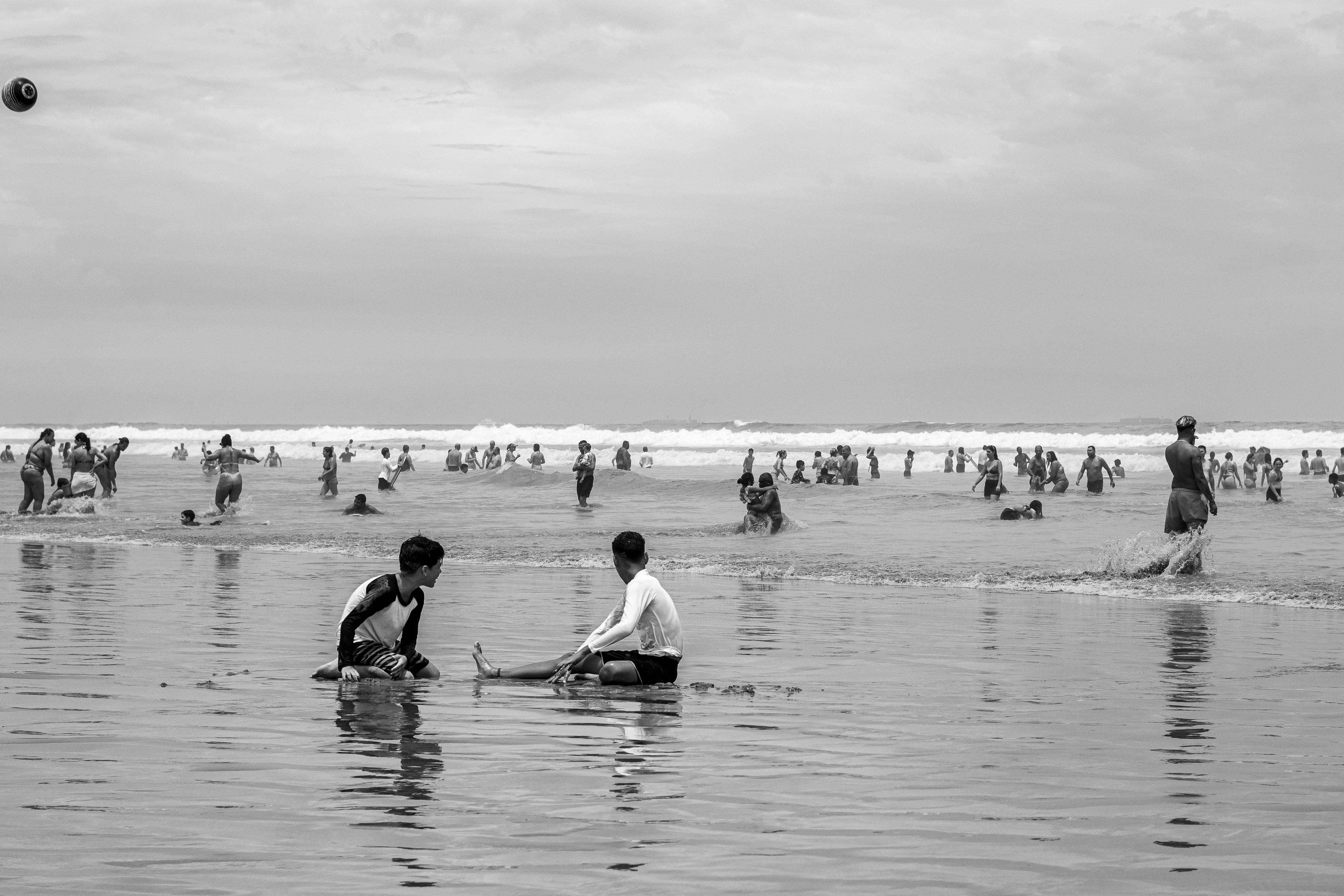 Two children netting shallow sea creatures as crowds gather on the horizon