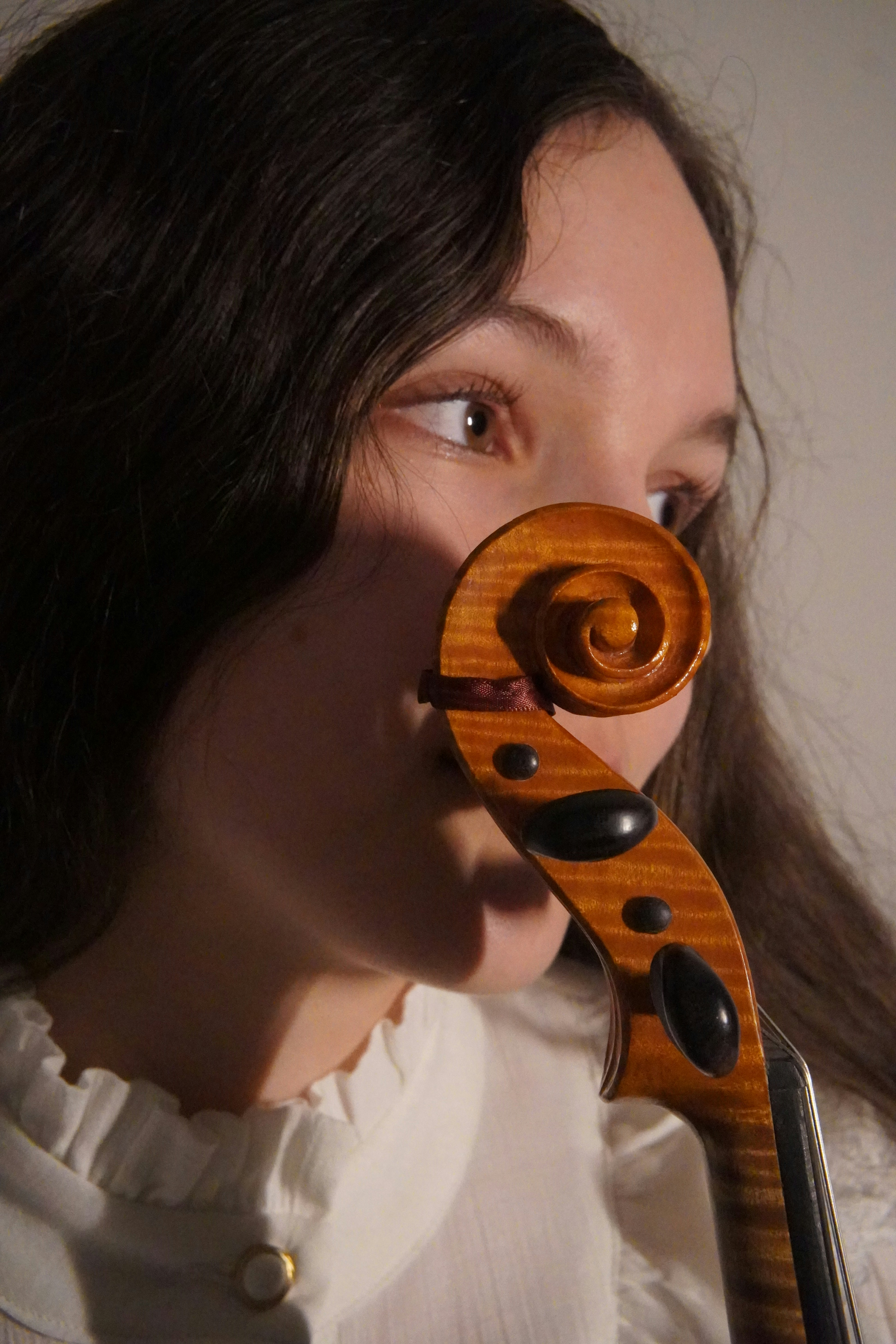 Face peeks from behind a cello scroll in warm light