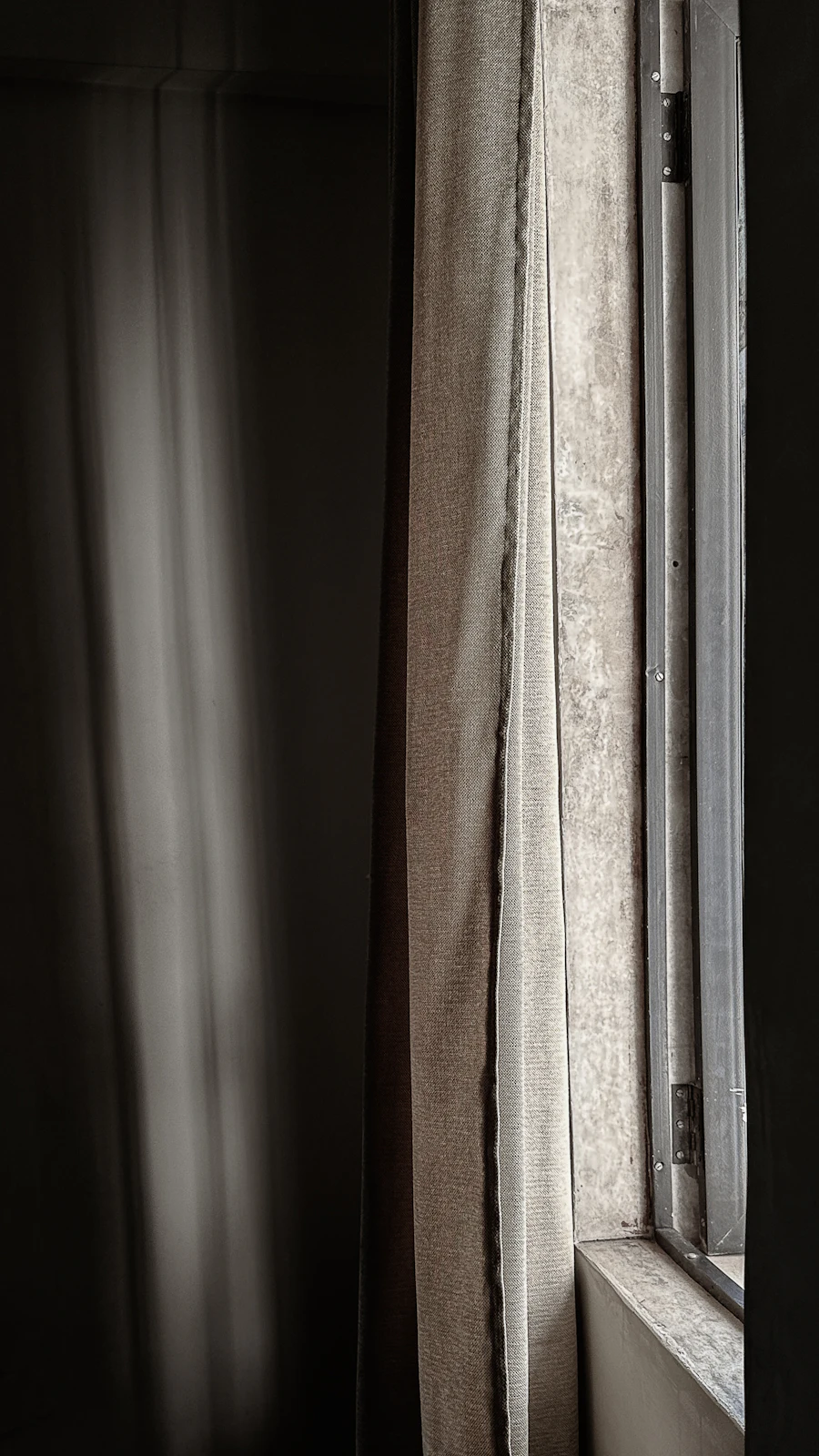 Softly lit window corner with layered curtains and a metal window frame, emphasizing texture and vertical lines.