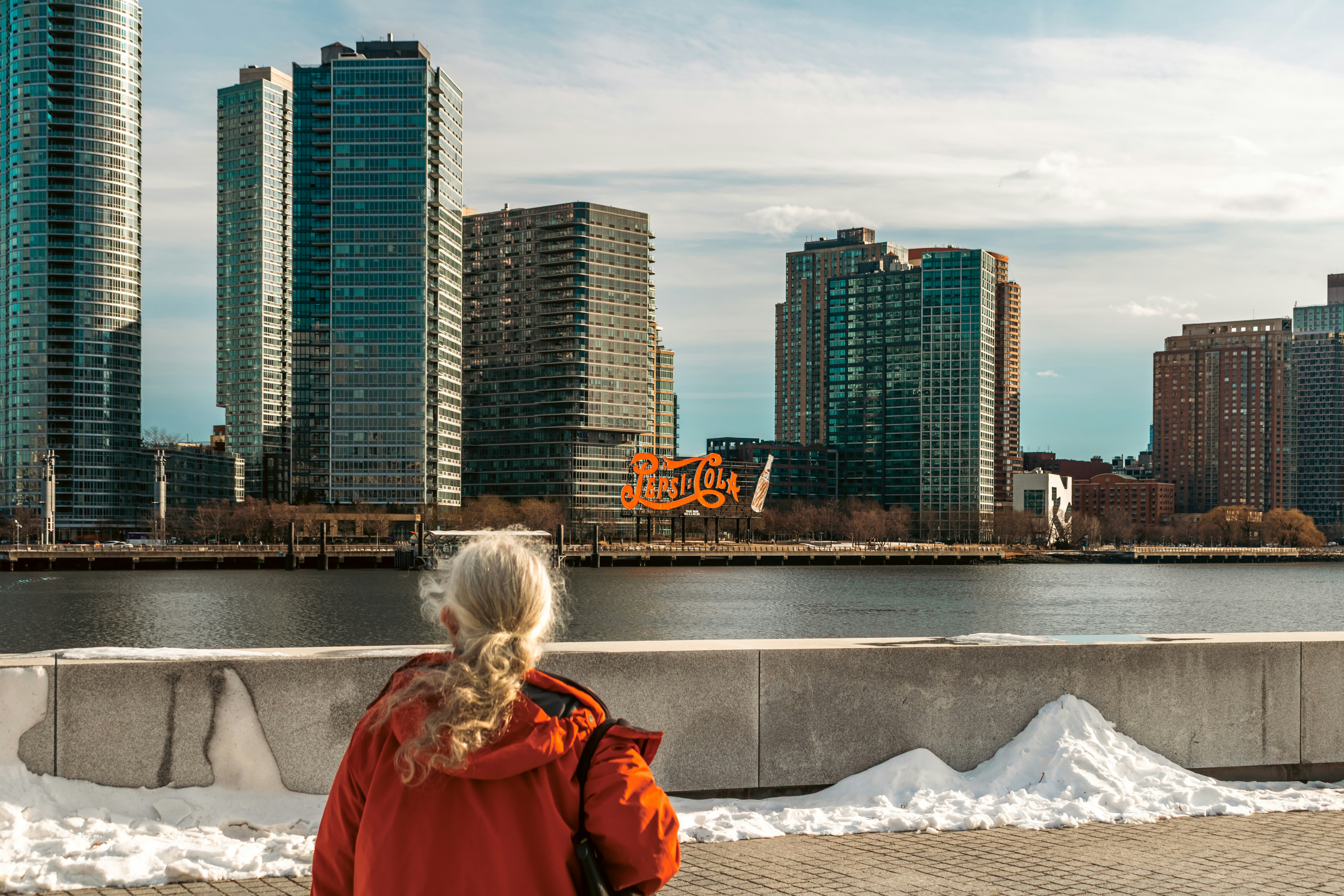 Riverfront Portrait: A Seeker in Red Against Glass Towers