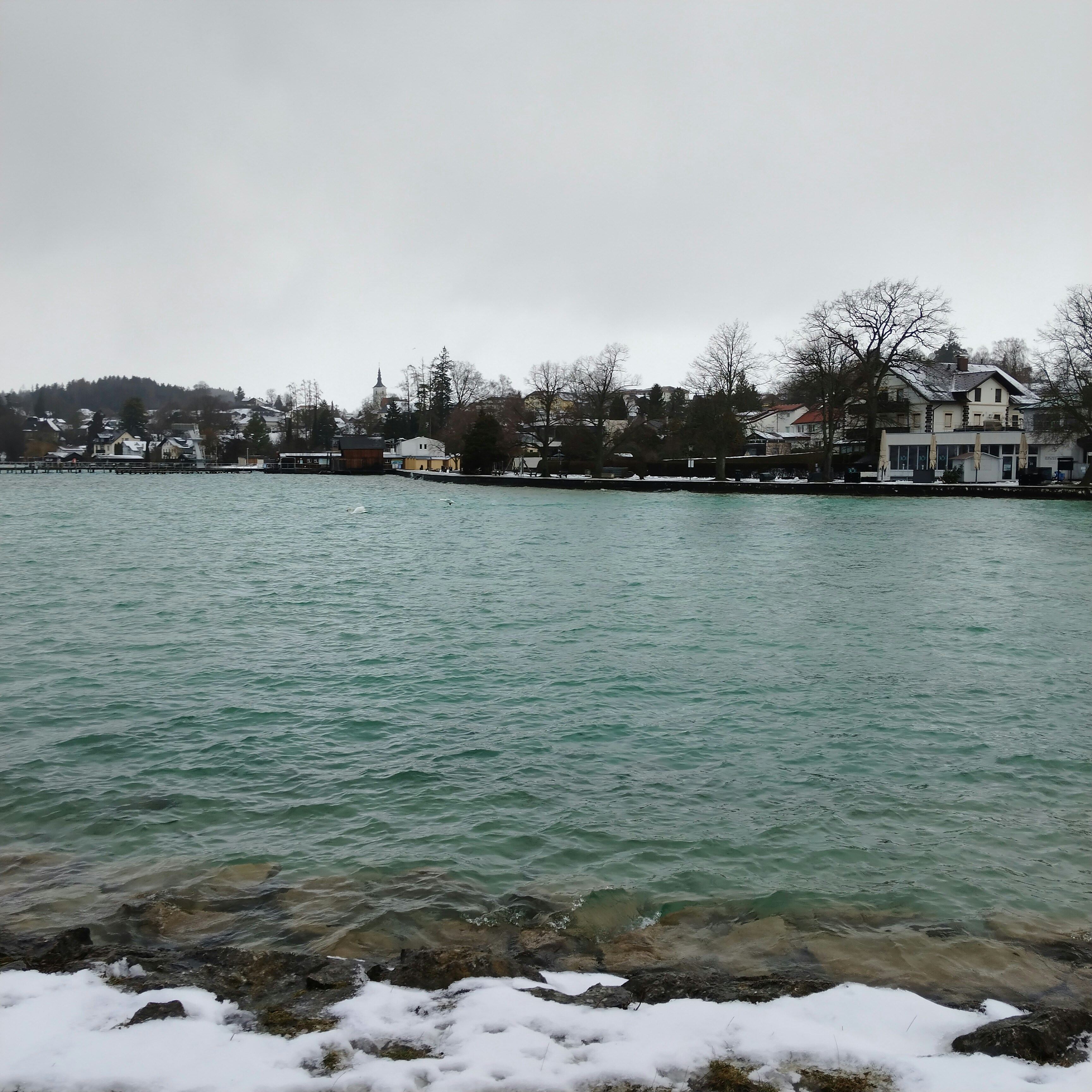 Turquoise water with snow-covered shore and houses.