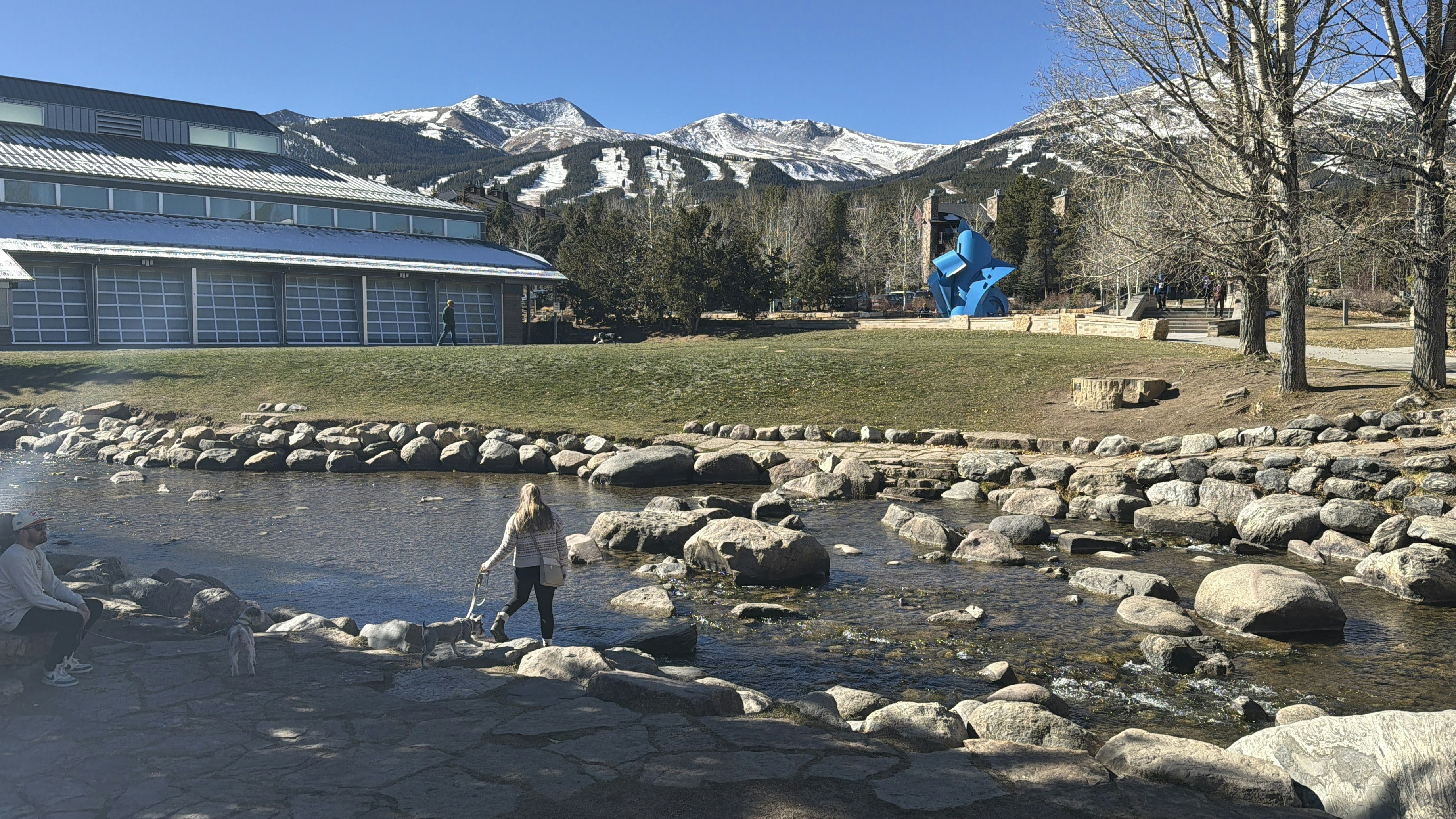 A person walks across rocks in a stream near mountains. photo – Free ...