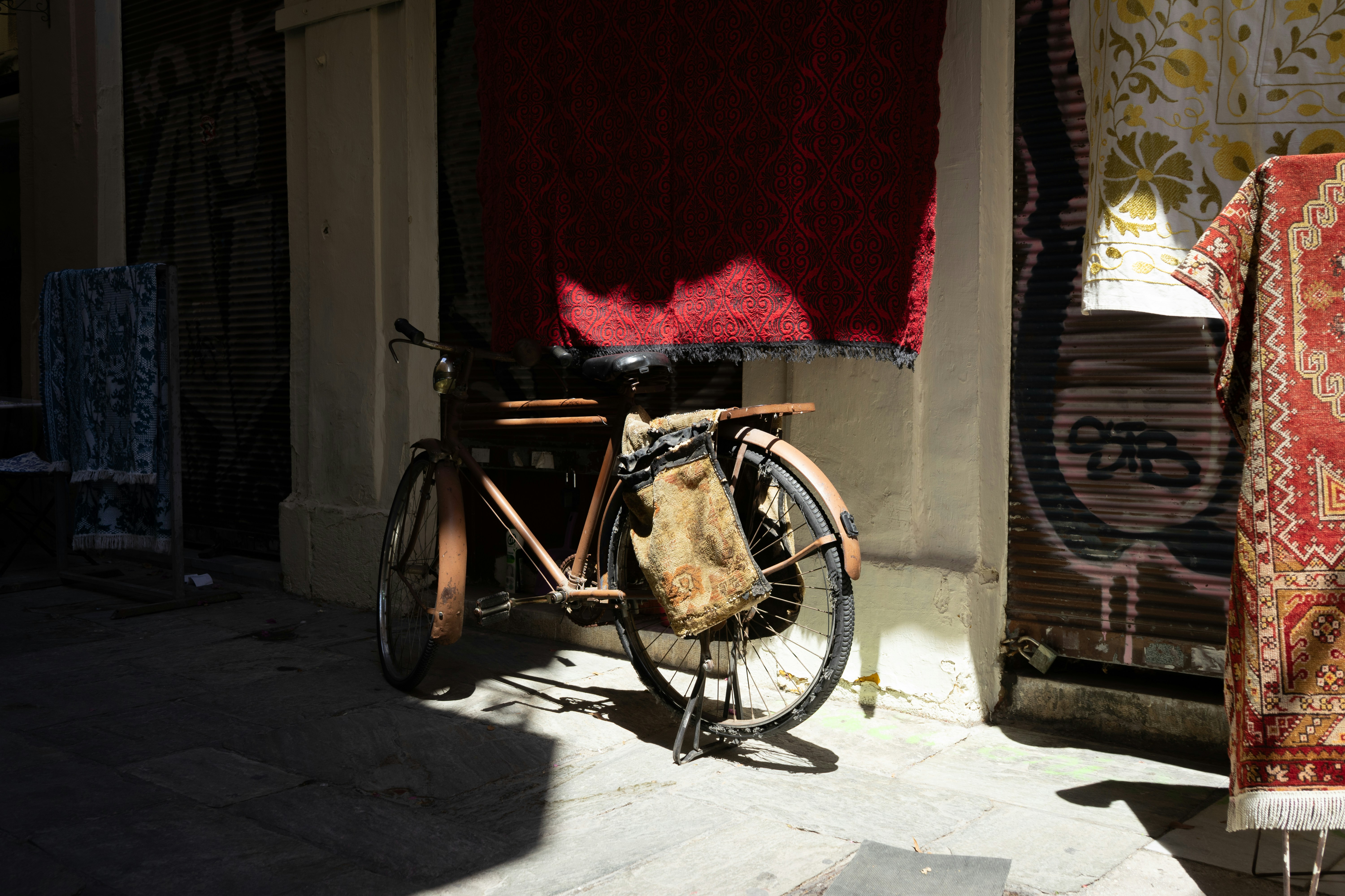Sunlit bicycle and hanging rugs in a sun-dappled alley