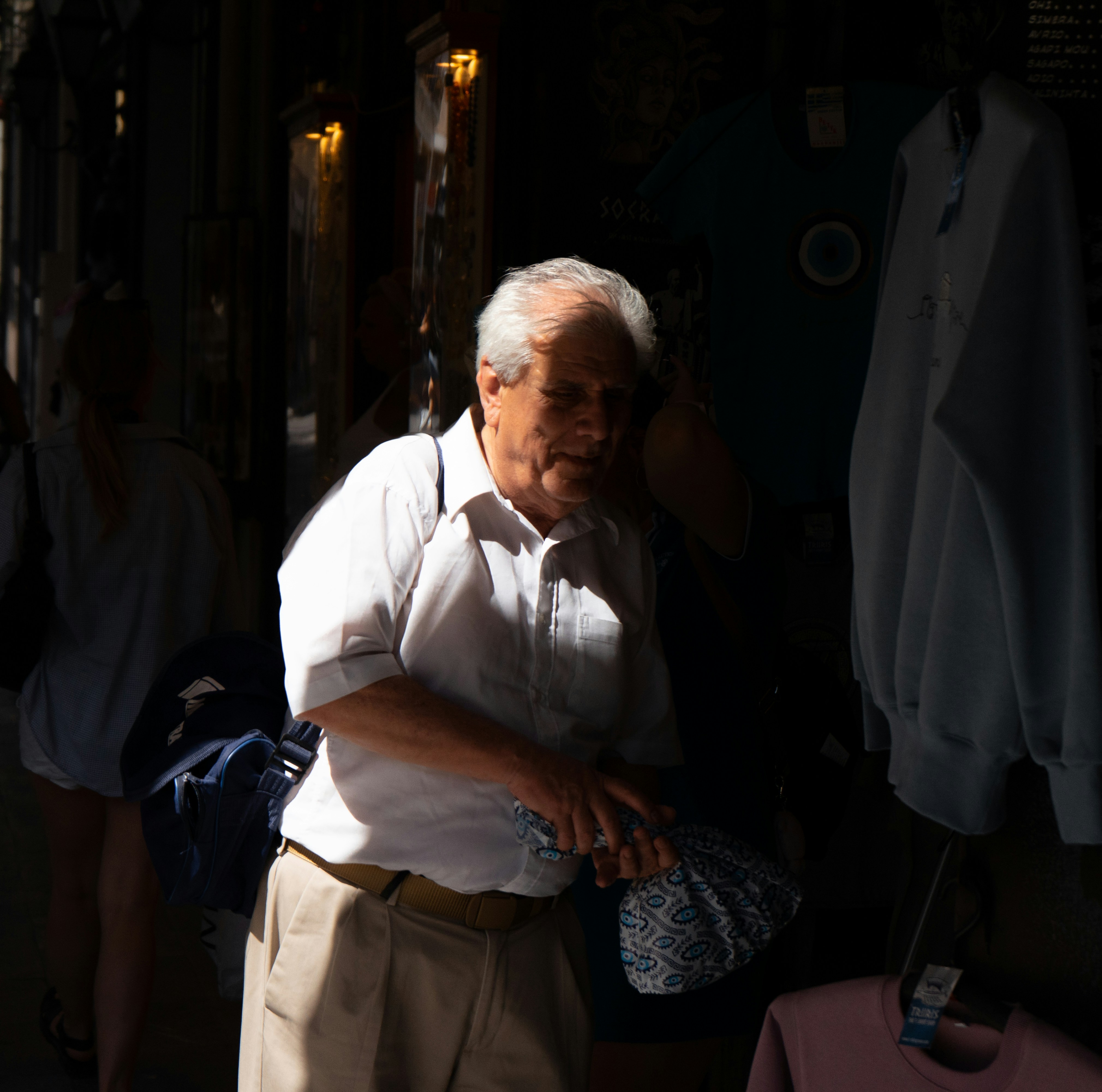 White‑haired man in a sunlit doorway, adjusting a patterned bag
