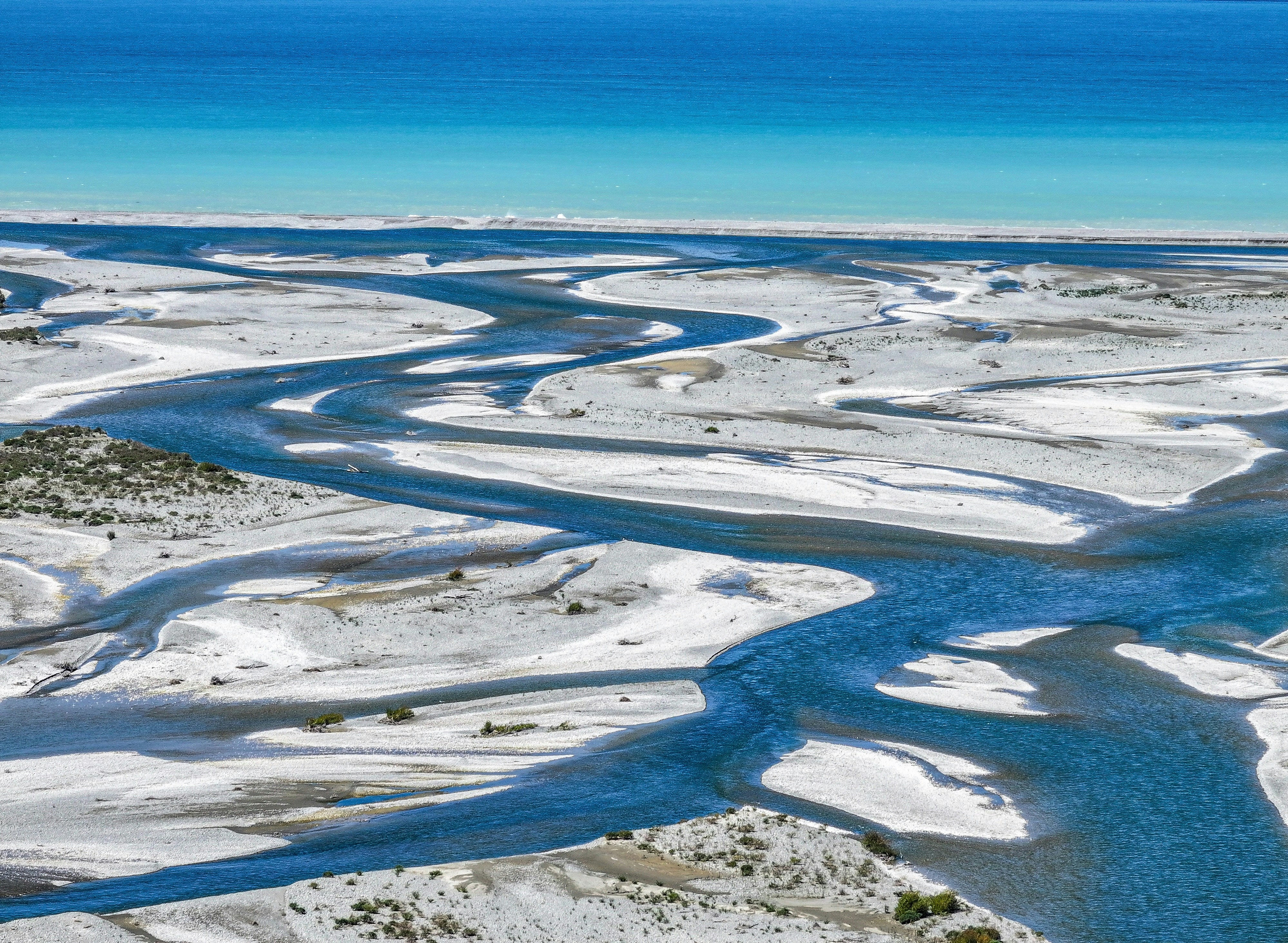 Winding blue river flowing through sandy landscape towards ocean