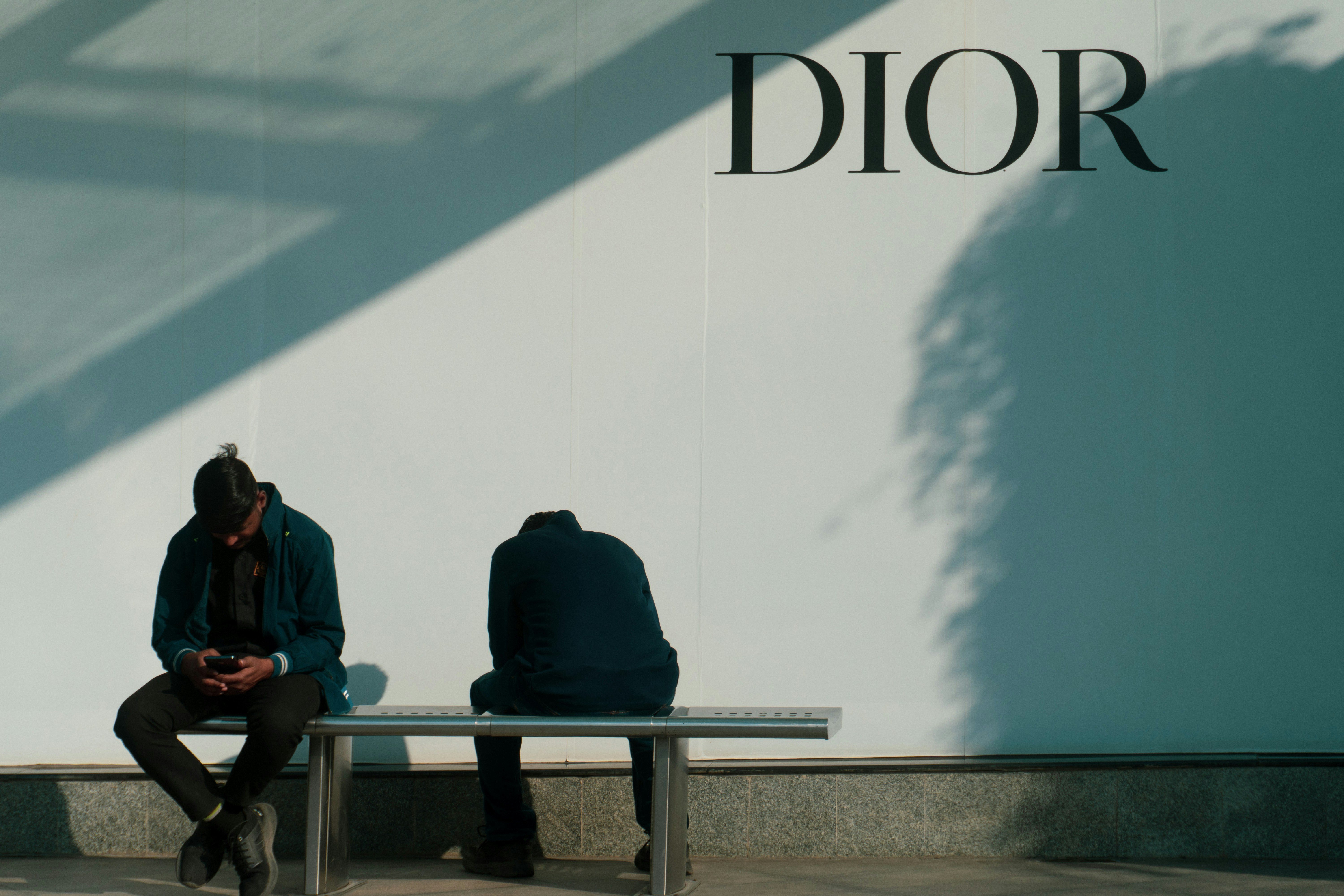 Quiet City Bench: Two Figures Against a Dior Wall
