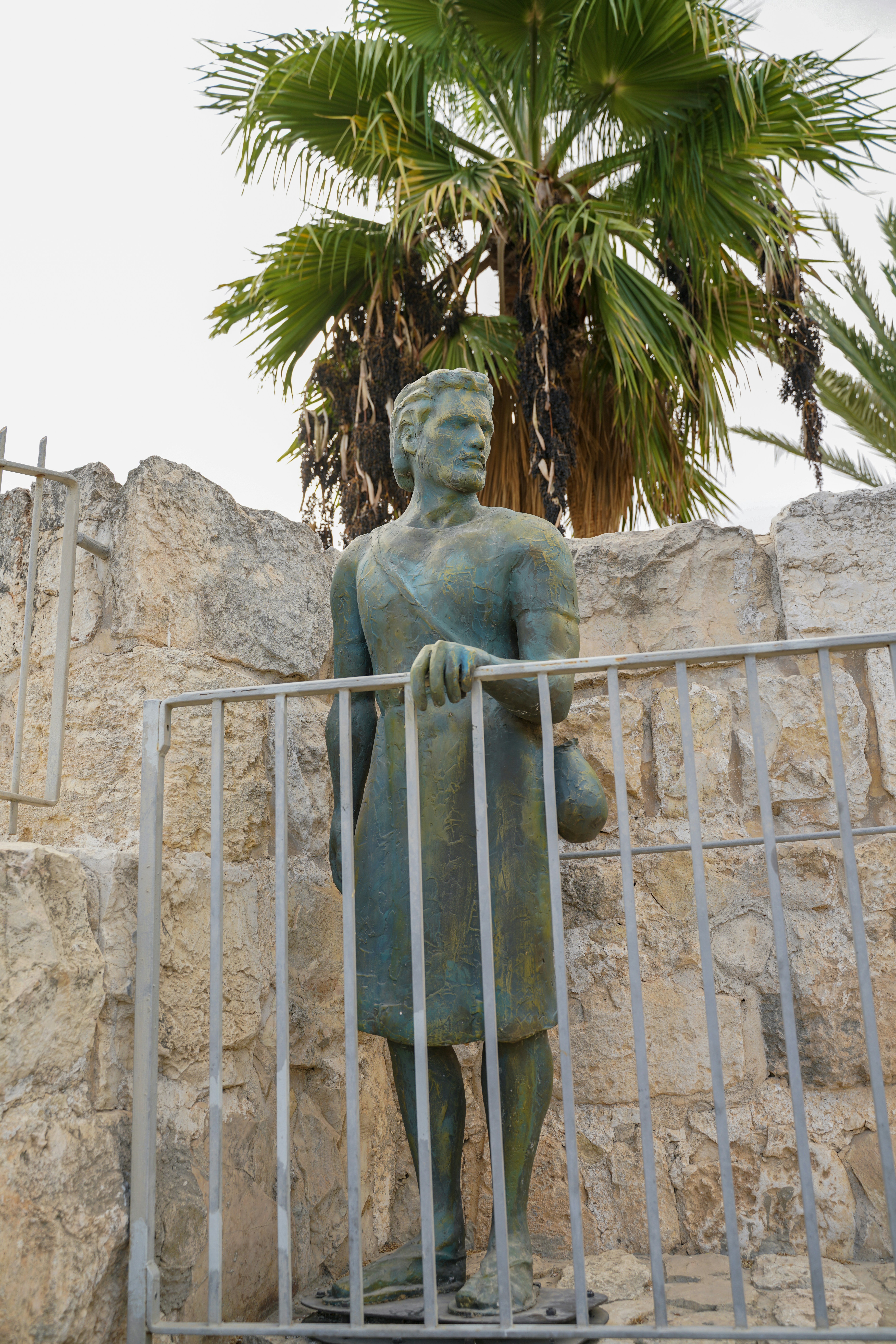 Guarding the Palm Terrace: Bronze Figure Behind Rough Quarry Walls