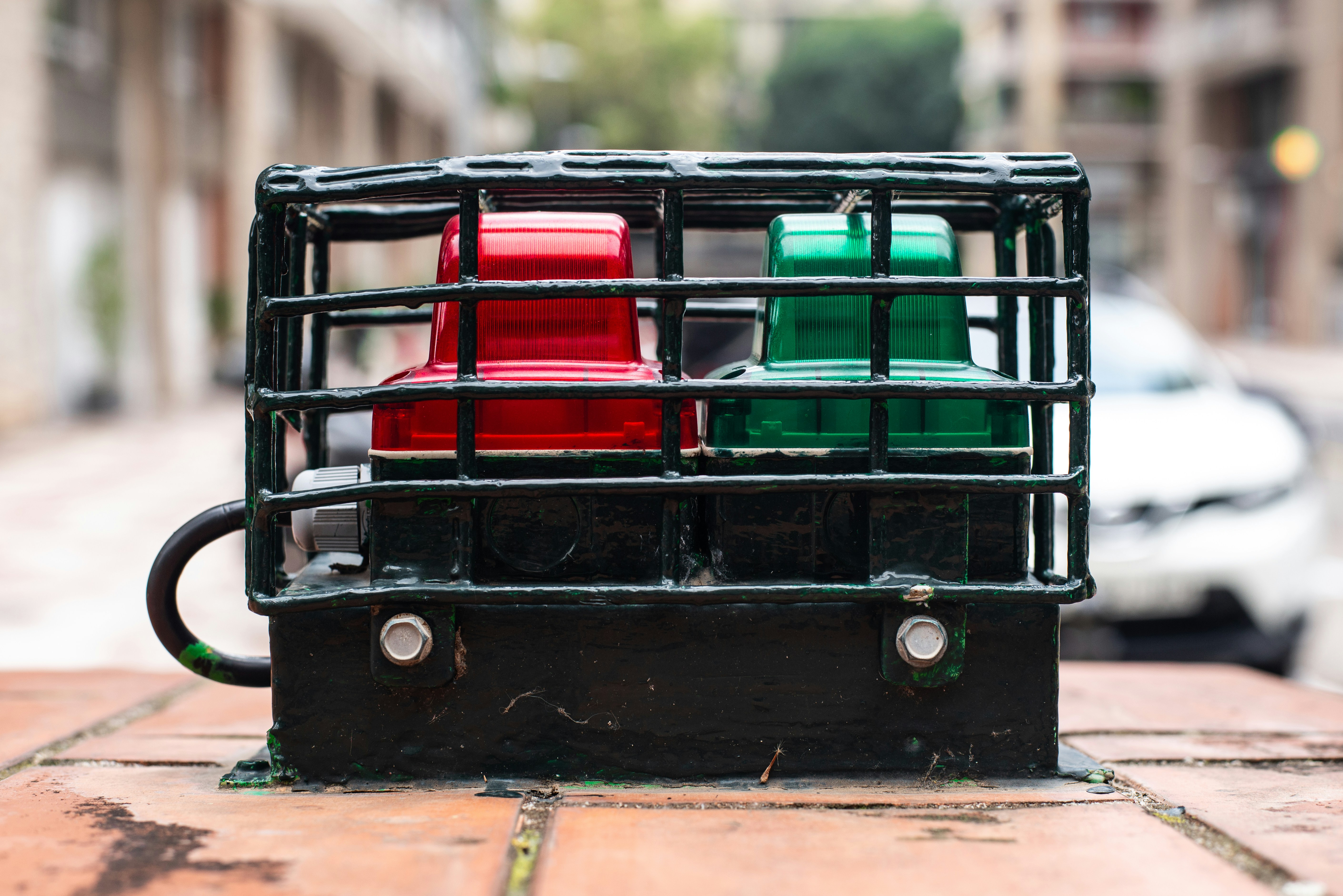 Red and Green Brake Lights Guarded by a Black Grate on a Brick Pedestal