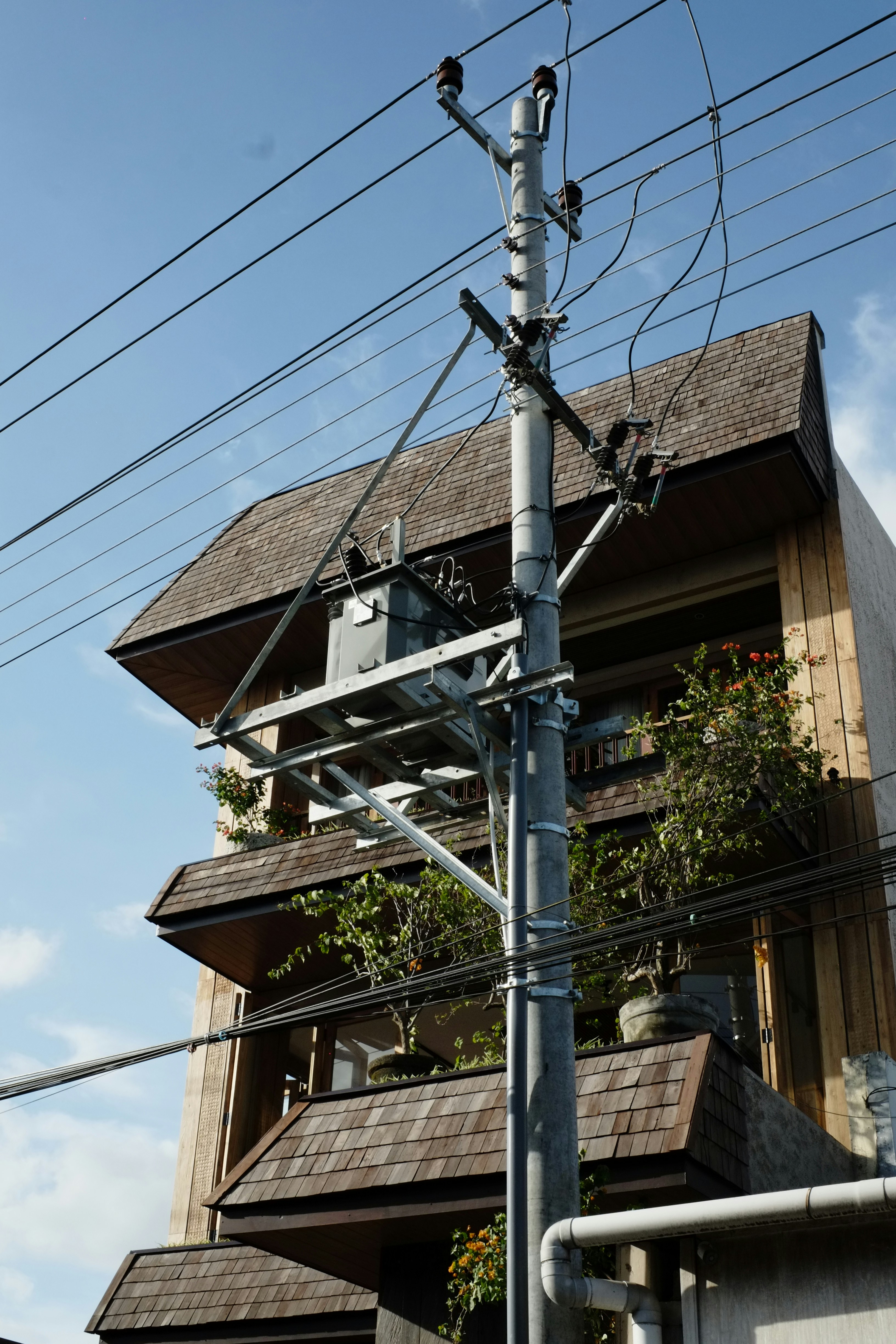 Utility Vertical: A Steel Mast Straddling Wooden Facades Under Blue Sky