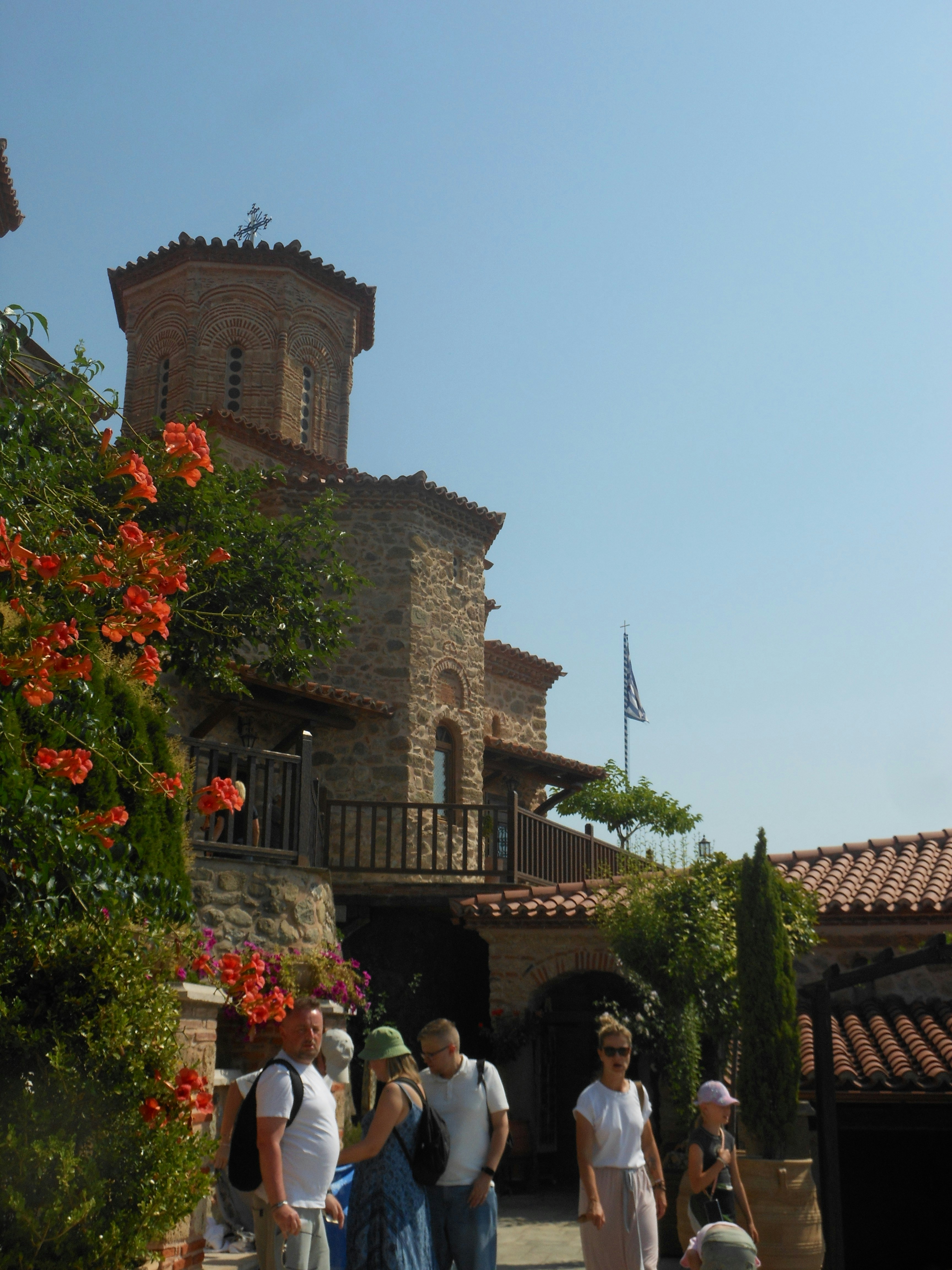 Tourists visit ancient stone monastery with blooming flowers.