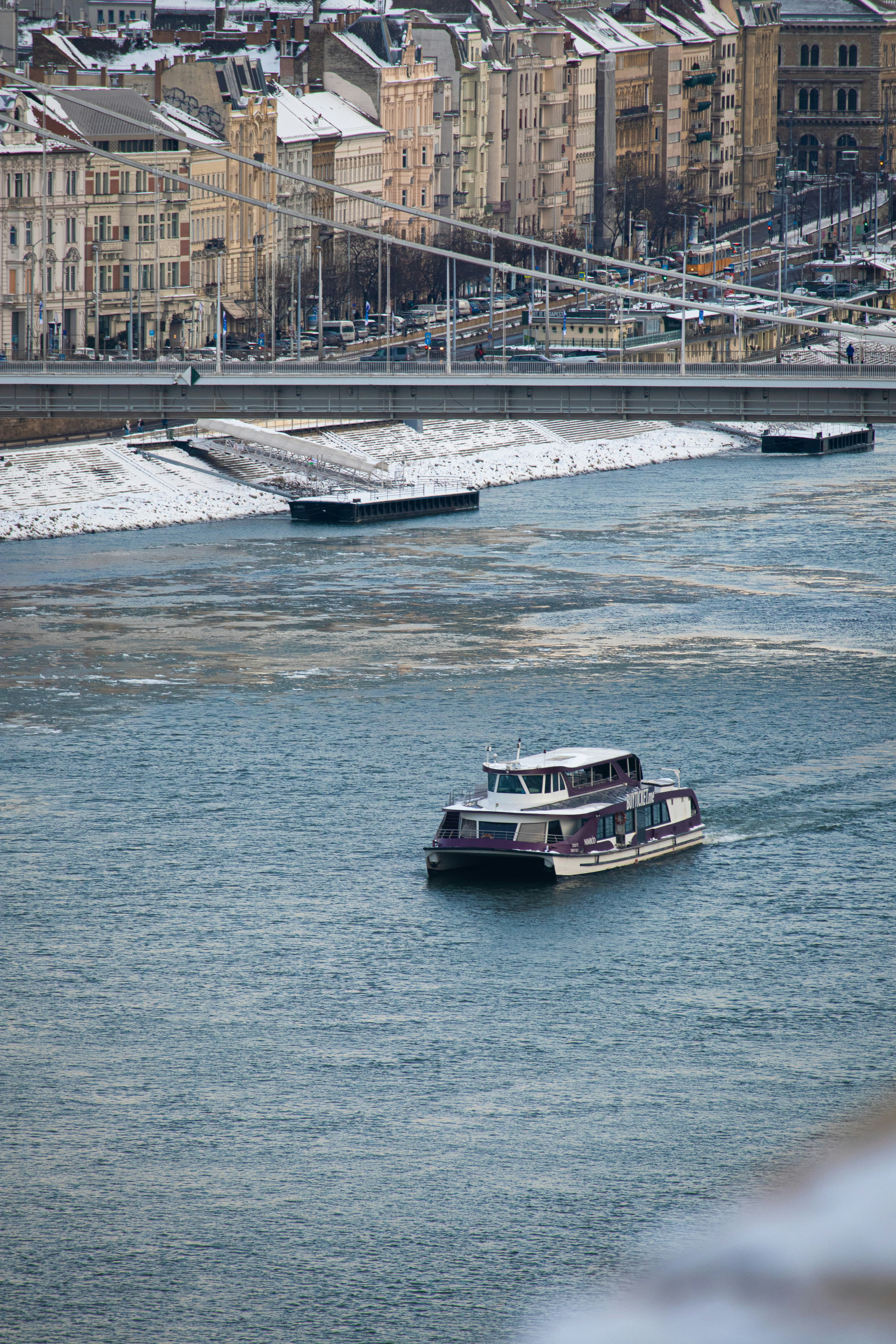City Boat on a Snow-Silvered River Under a Cable-Strewn Bridge