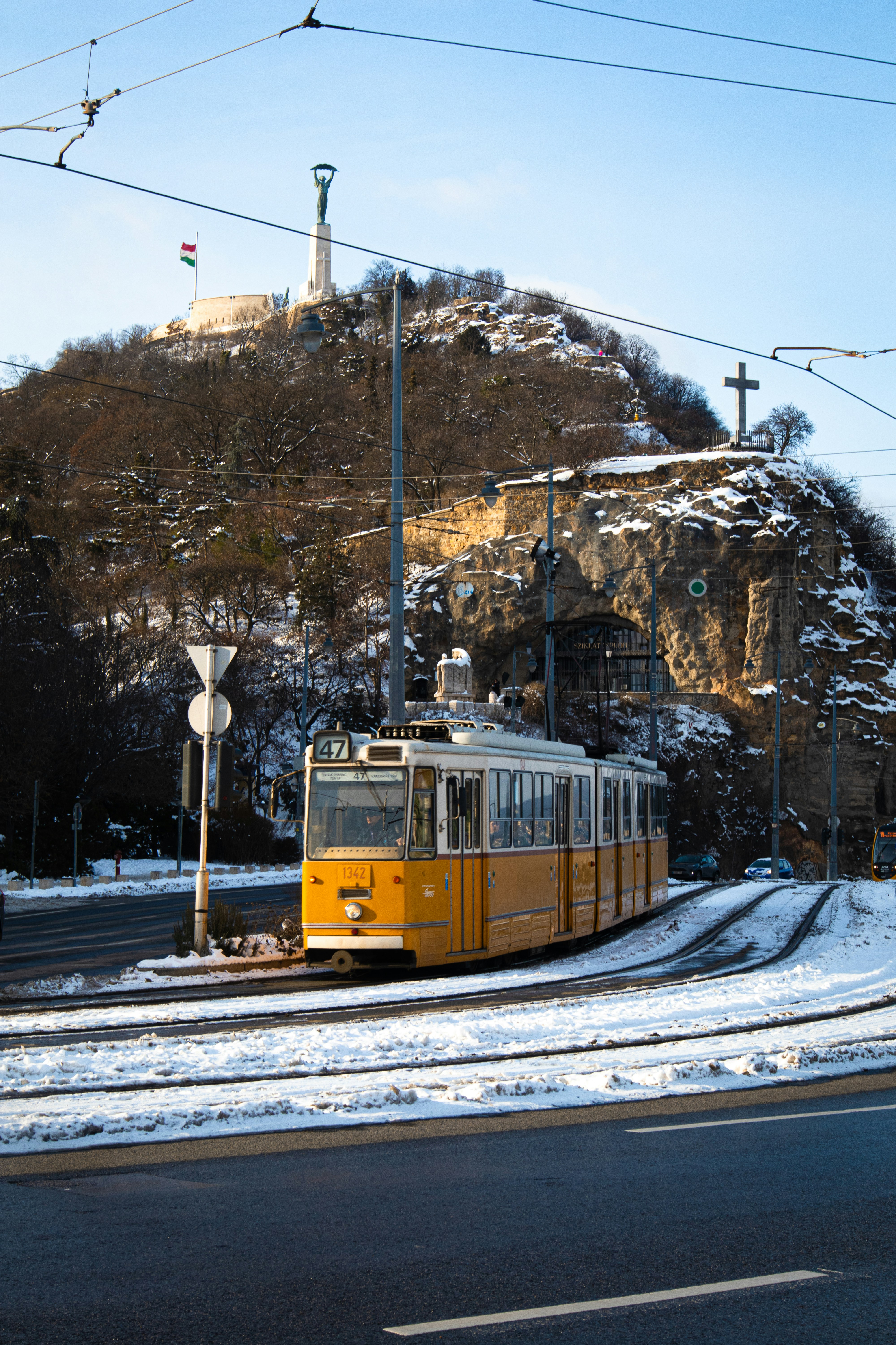 Yellow tram crossing snowy rails beneath a hilltop statue
