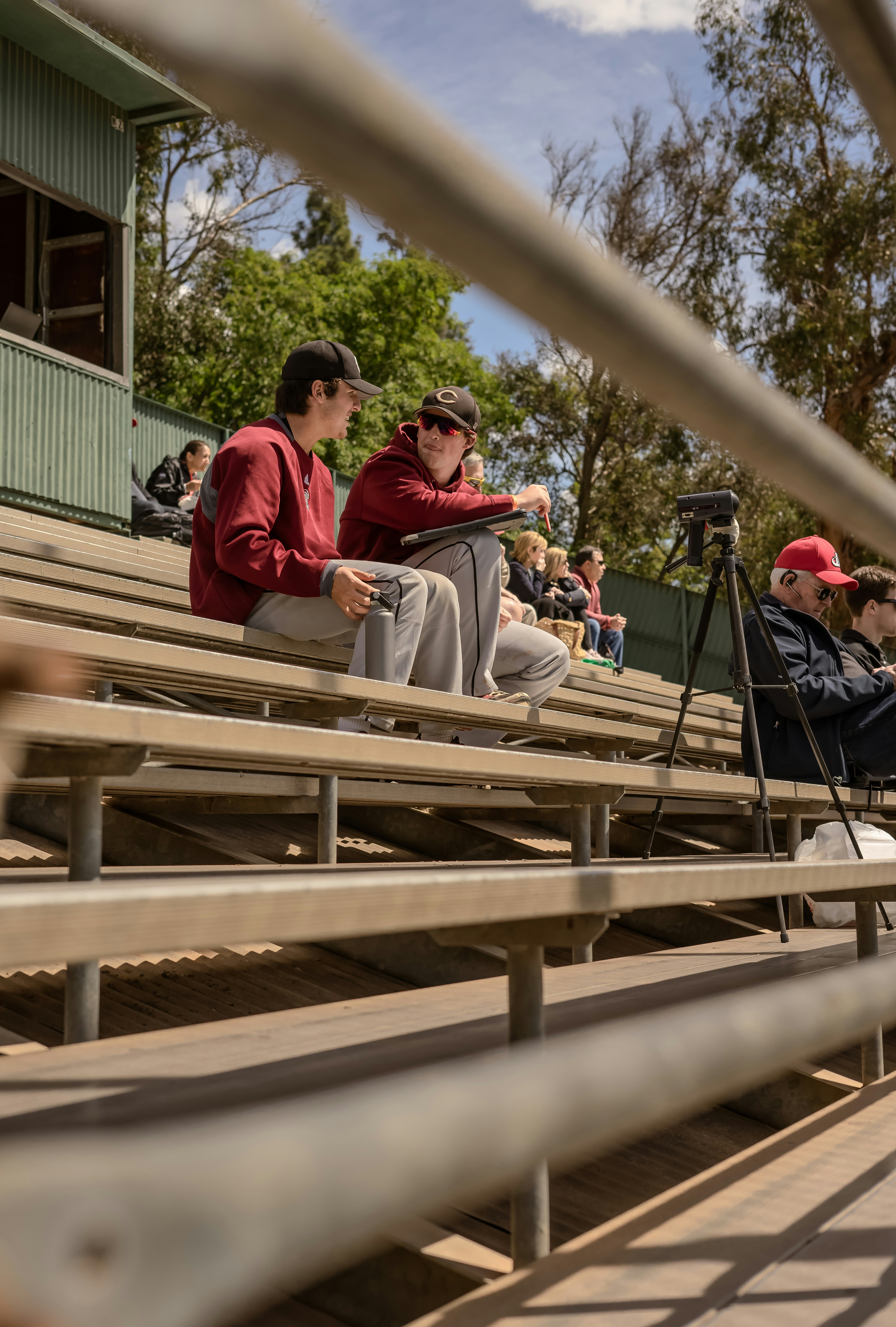 Two Coaches in Red Sweatshirts Share a Quiet Moment Under the Bleachers