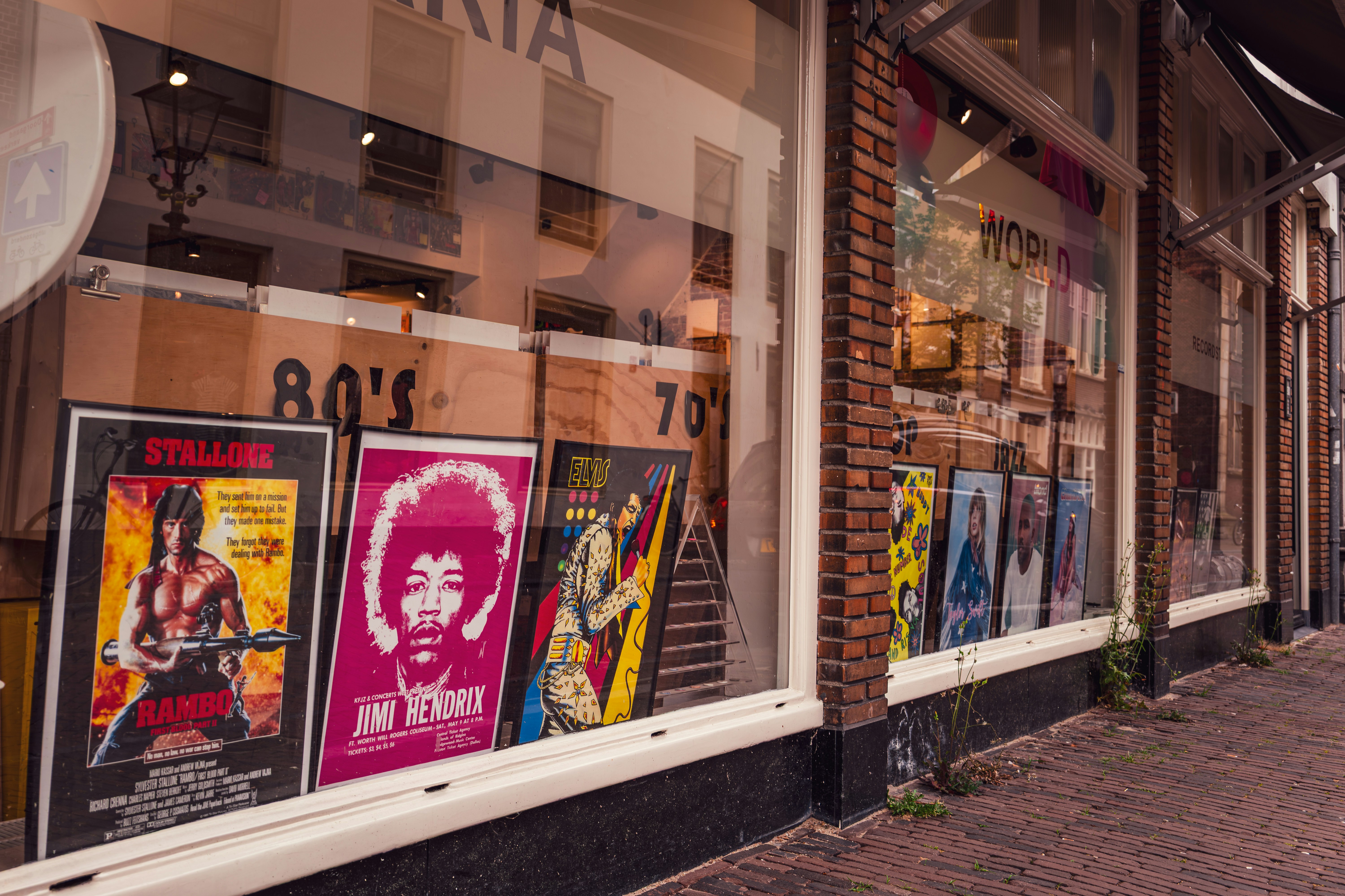 Record store window in Utrecht, Netherlands, displaying classic music and movie posters along a historic brick street.