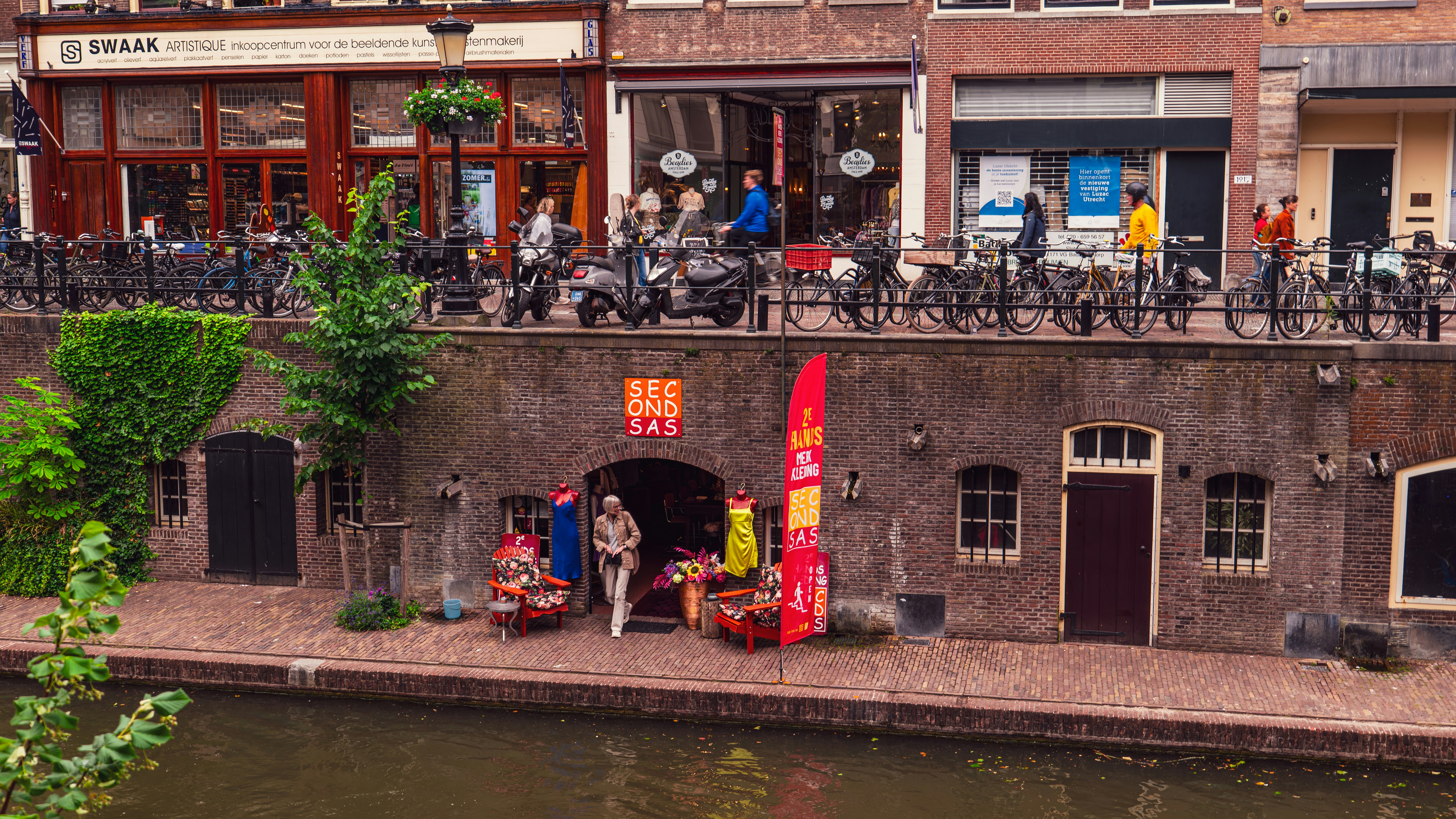 Second-hand clothing shop along the Oudegracht canal in Utrecht, Netherlands, with historic brick wharf cellars and bicycles above.