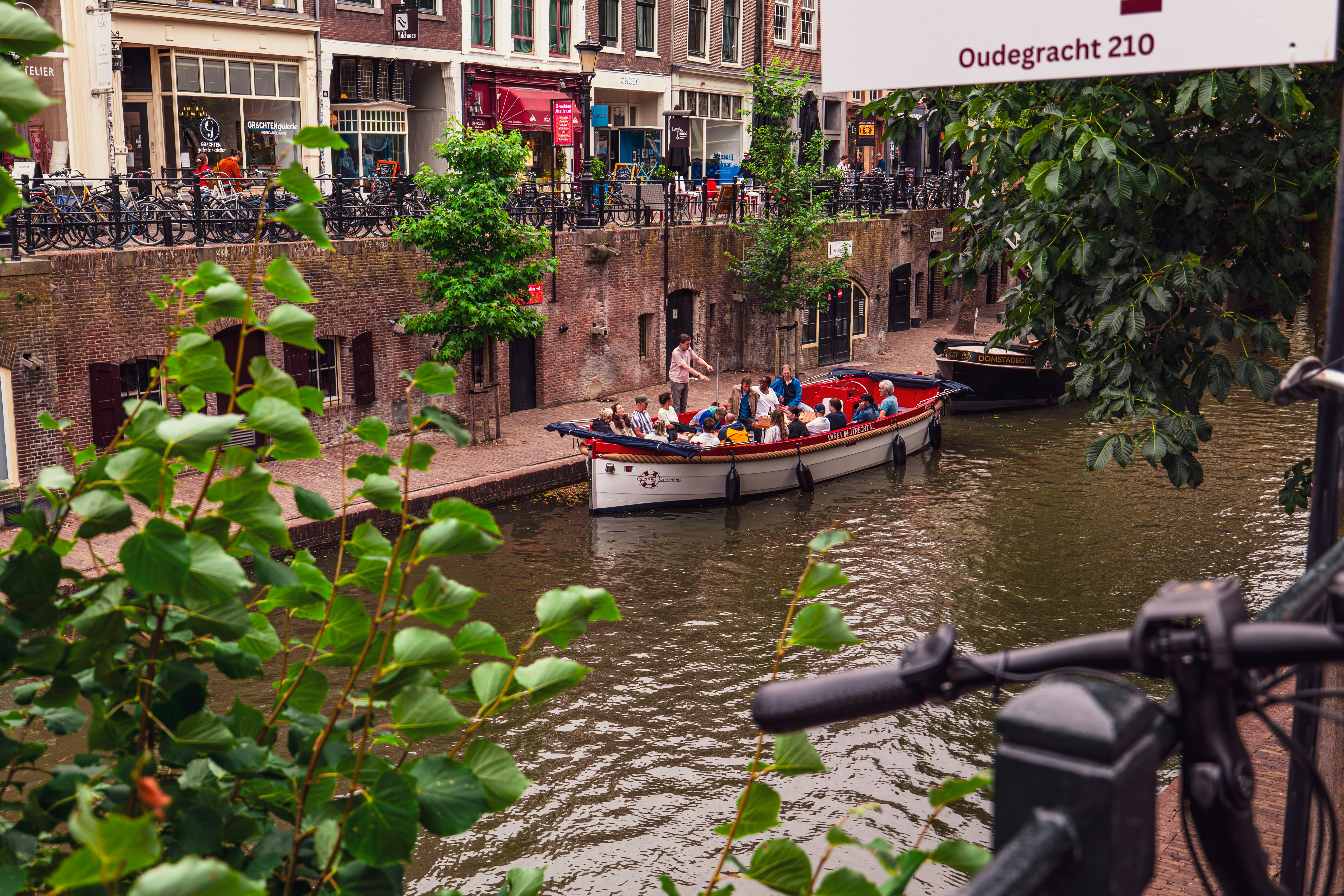 Canal boat tour on the Oudegracht at Oudegracht 210 in Utrecht, Netherlands, with historic wharf cellars and city life along the water.