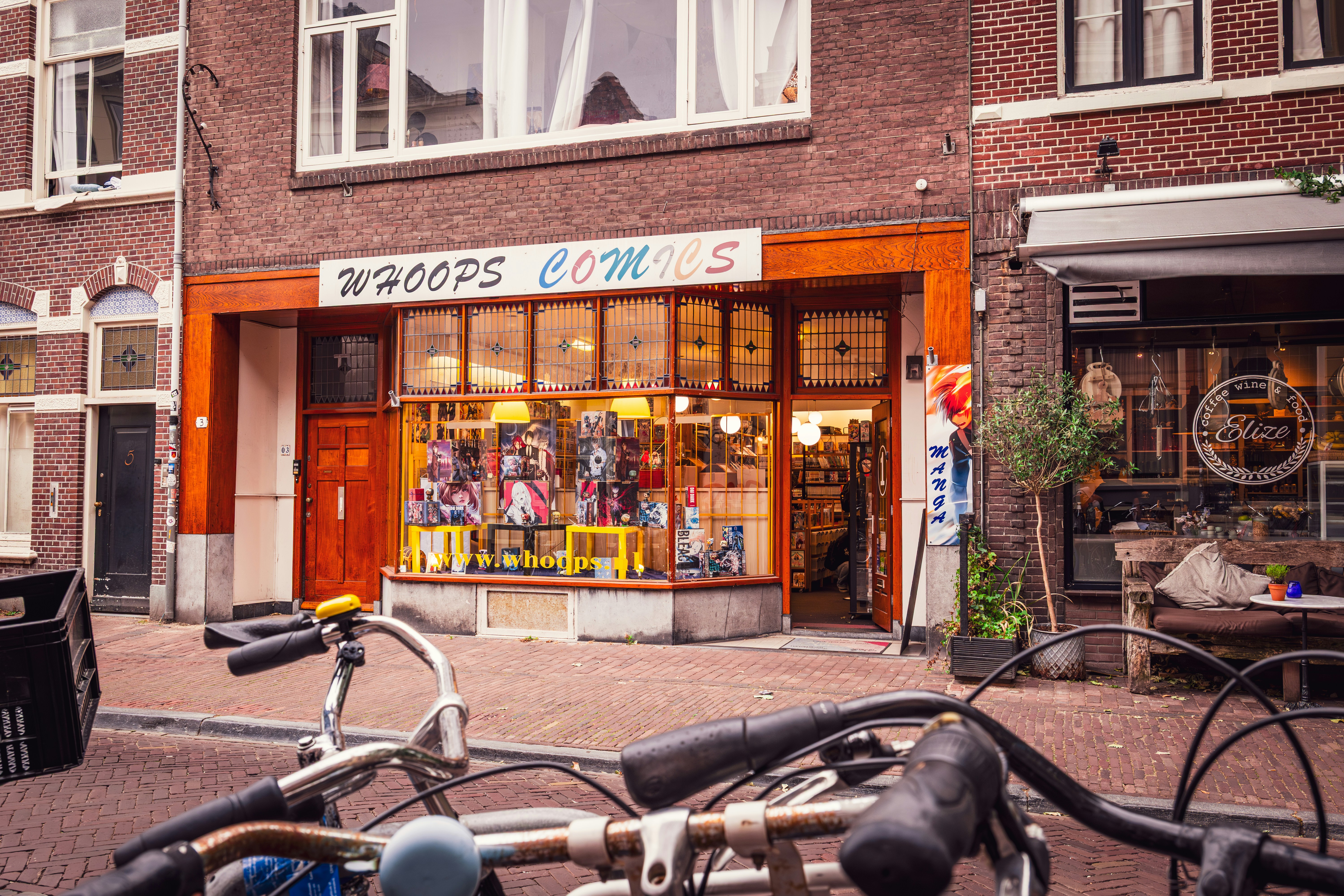 Exterior of Whoops Comics, a comic book and manga shop in Utrecht, Netherlands, with a colorful storefront and bicycles parked along the street.