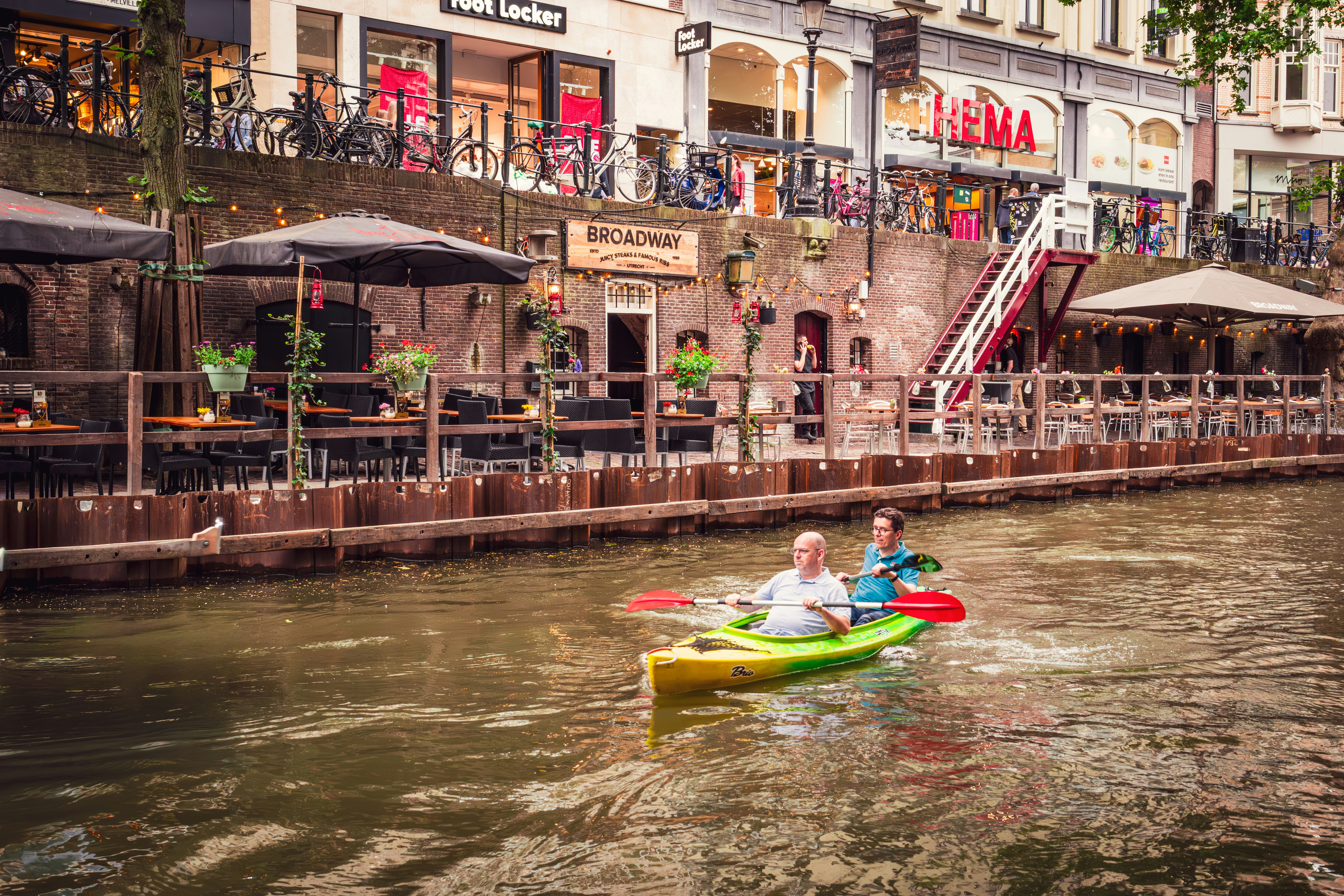 Two-Person Kayak Drifting Past a Canalfront Café in an Urban European Setting