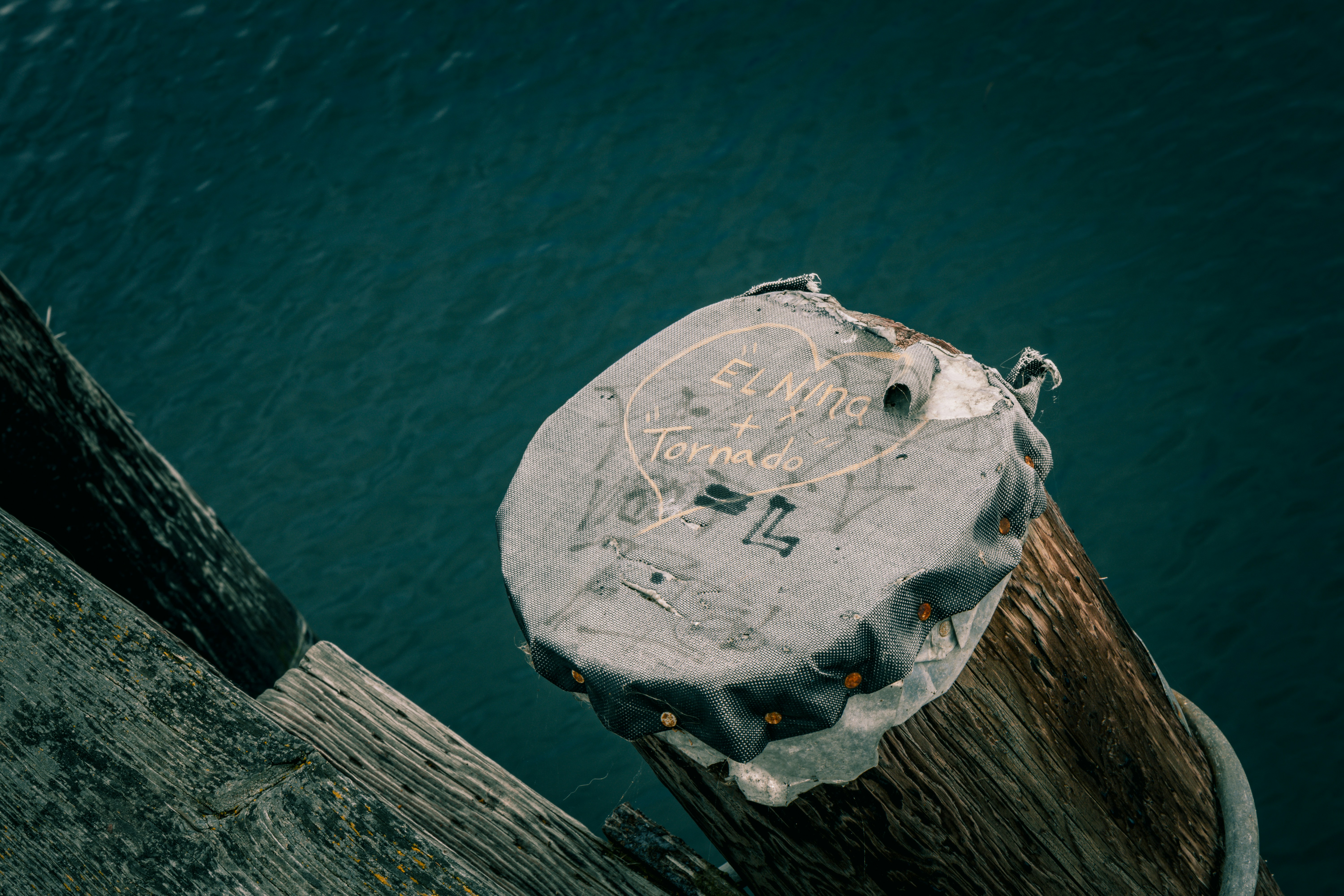 Weathered cap on a wooden mooring against teal sea