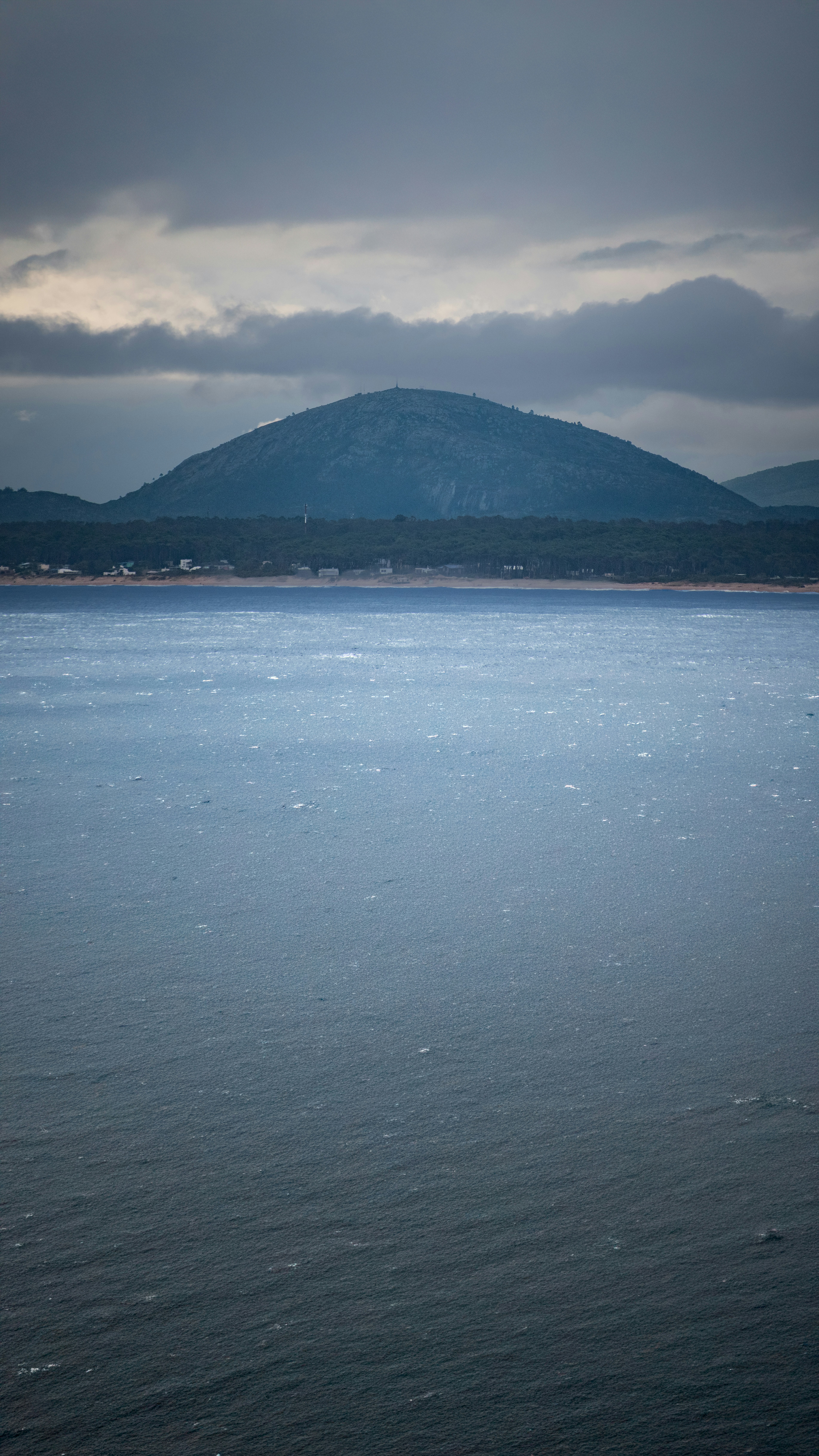 Quiet basalt hill rising from a slate-blue sea under a clouded sky