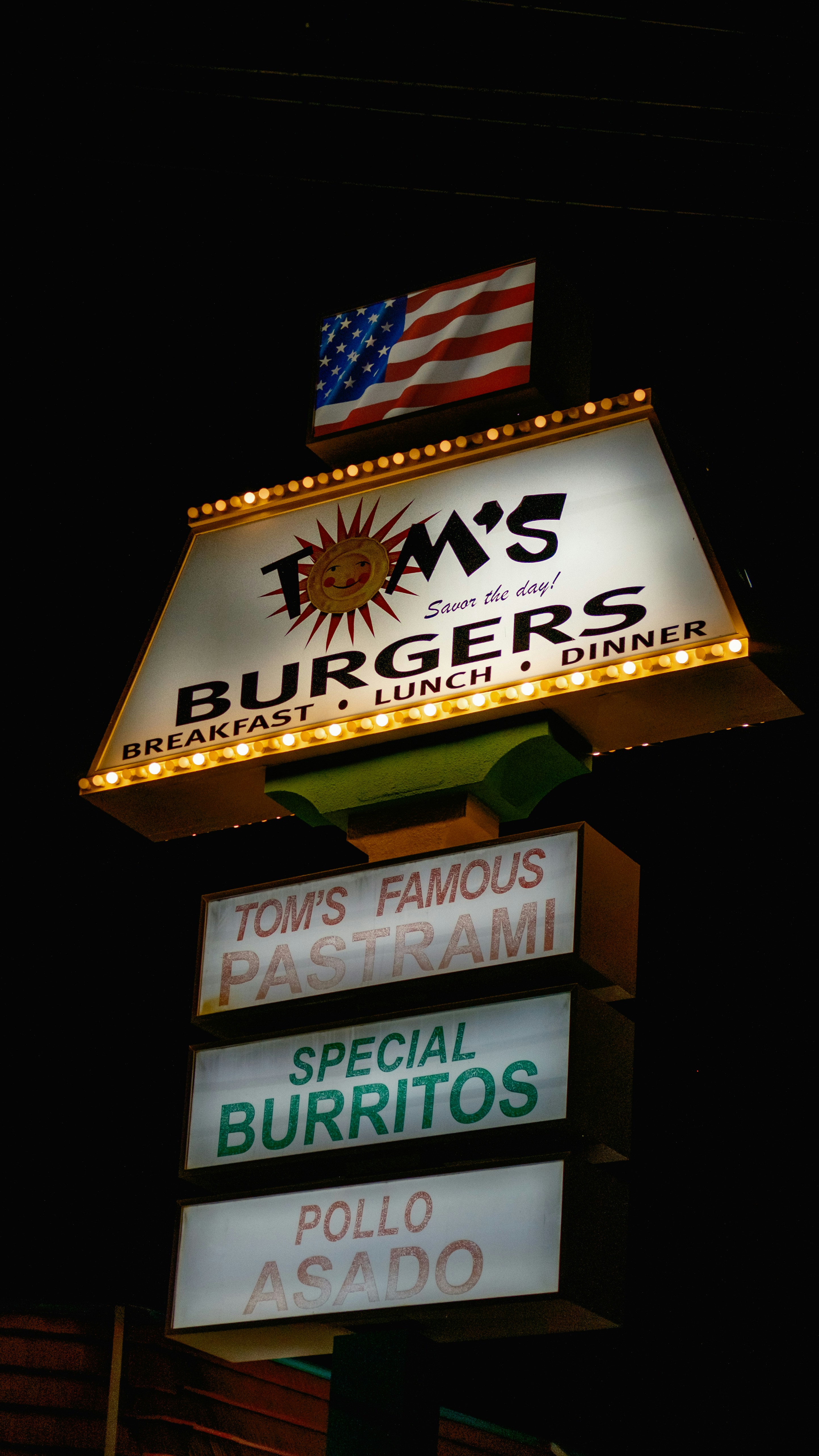 Tom's burgers sign with american flag at night.