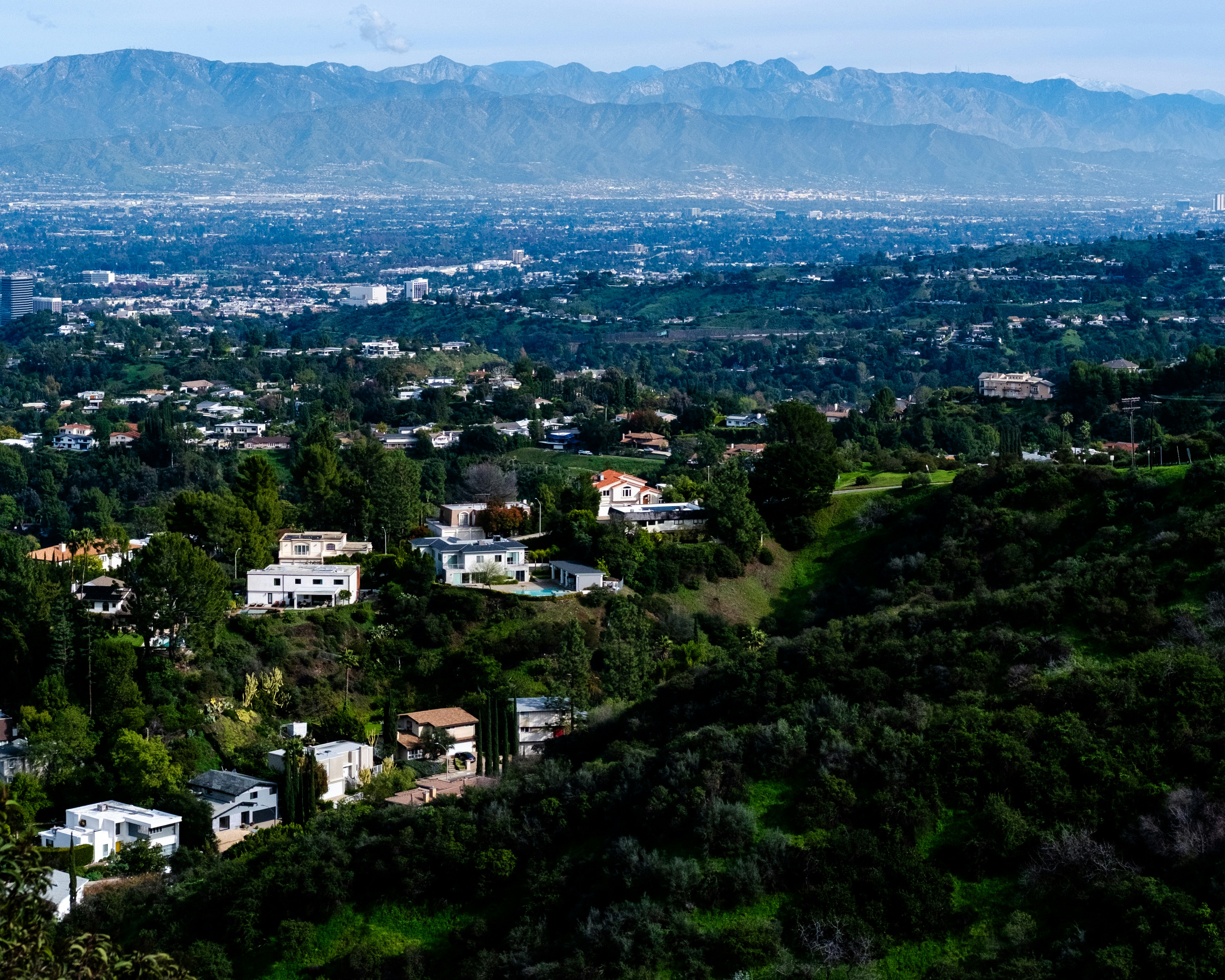 Suburban homes nestled in rolling green hills with mountains beyond.