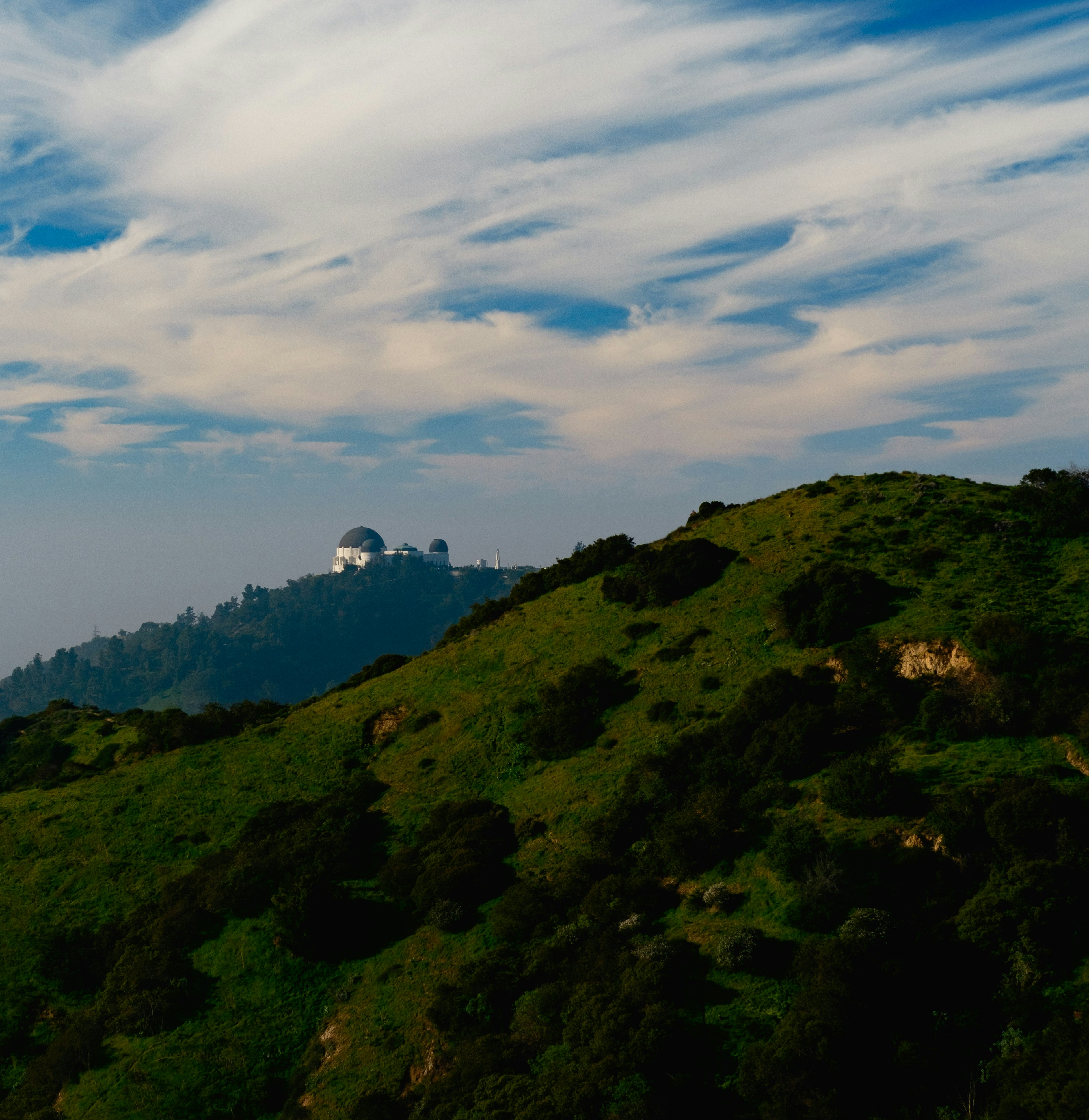 Griffith observatory sits atop a distant hill under clouds.