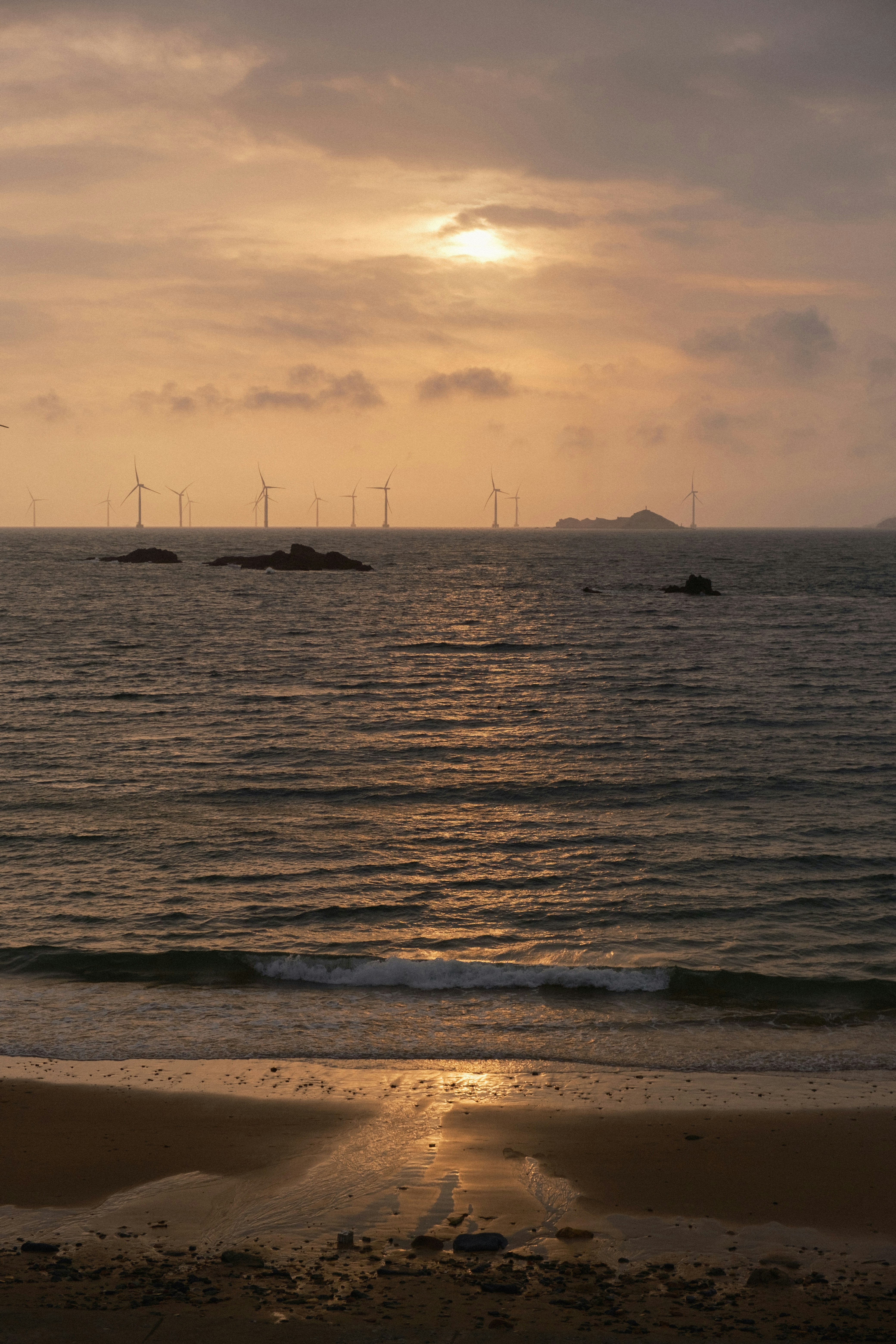 Golden Horizon: Wind Turbines Silhouetted at Dusk Over a Quiet Sea