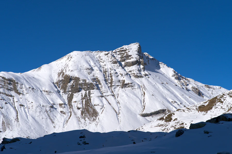 Snow-covered mountain peaks under a clear blue sky with shadowed foreground; a stark alpine landscape emphasizing texture and contrast. (Photographic landscape capture)