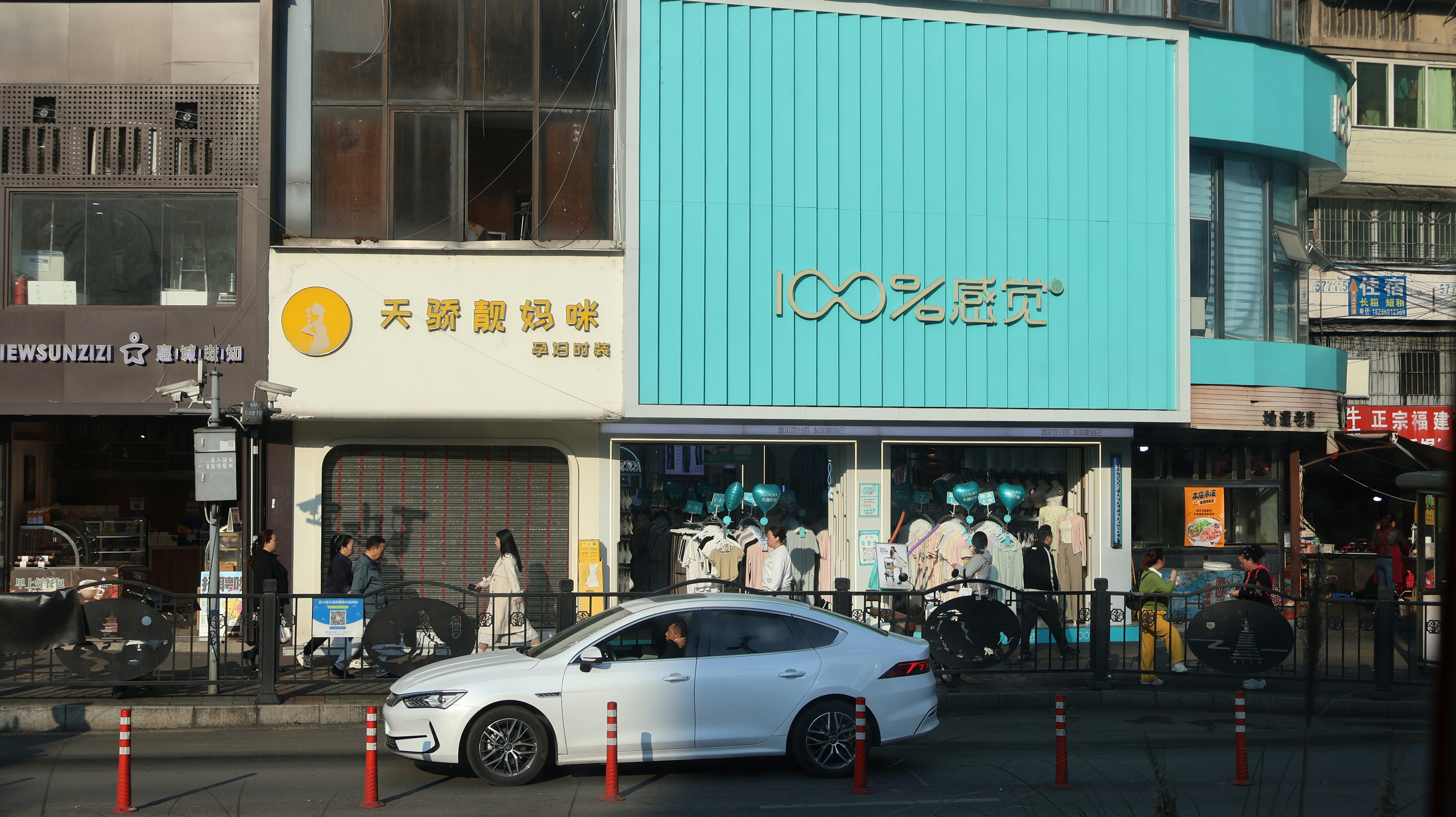 Glassy blue facade and a moving white sedan beneath urban storefronts