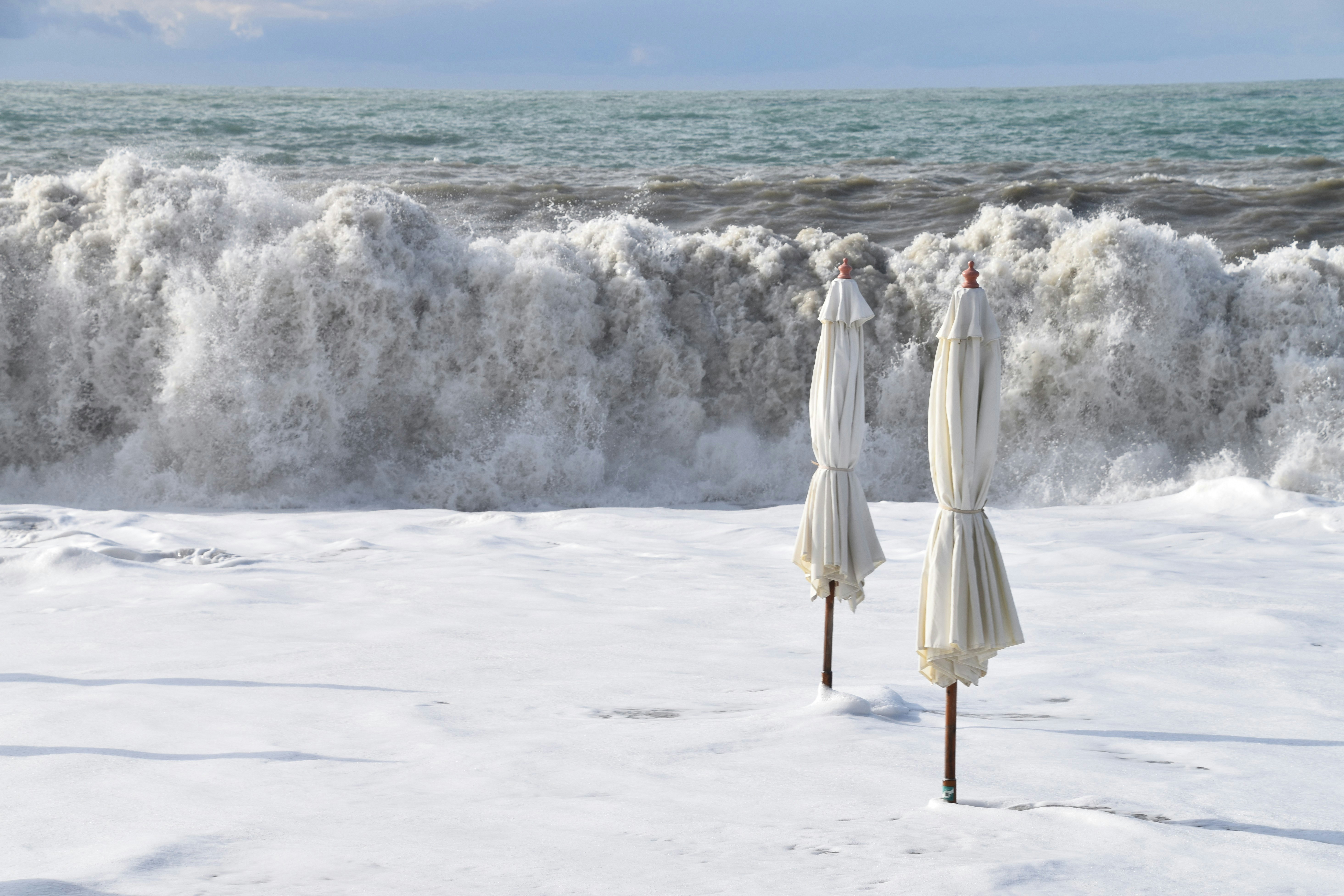 Sculpted Waves Meet Quiet Beach: Umbrellas Stand Against the Surf