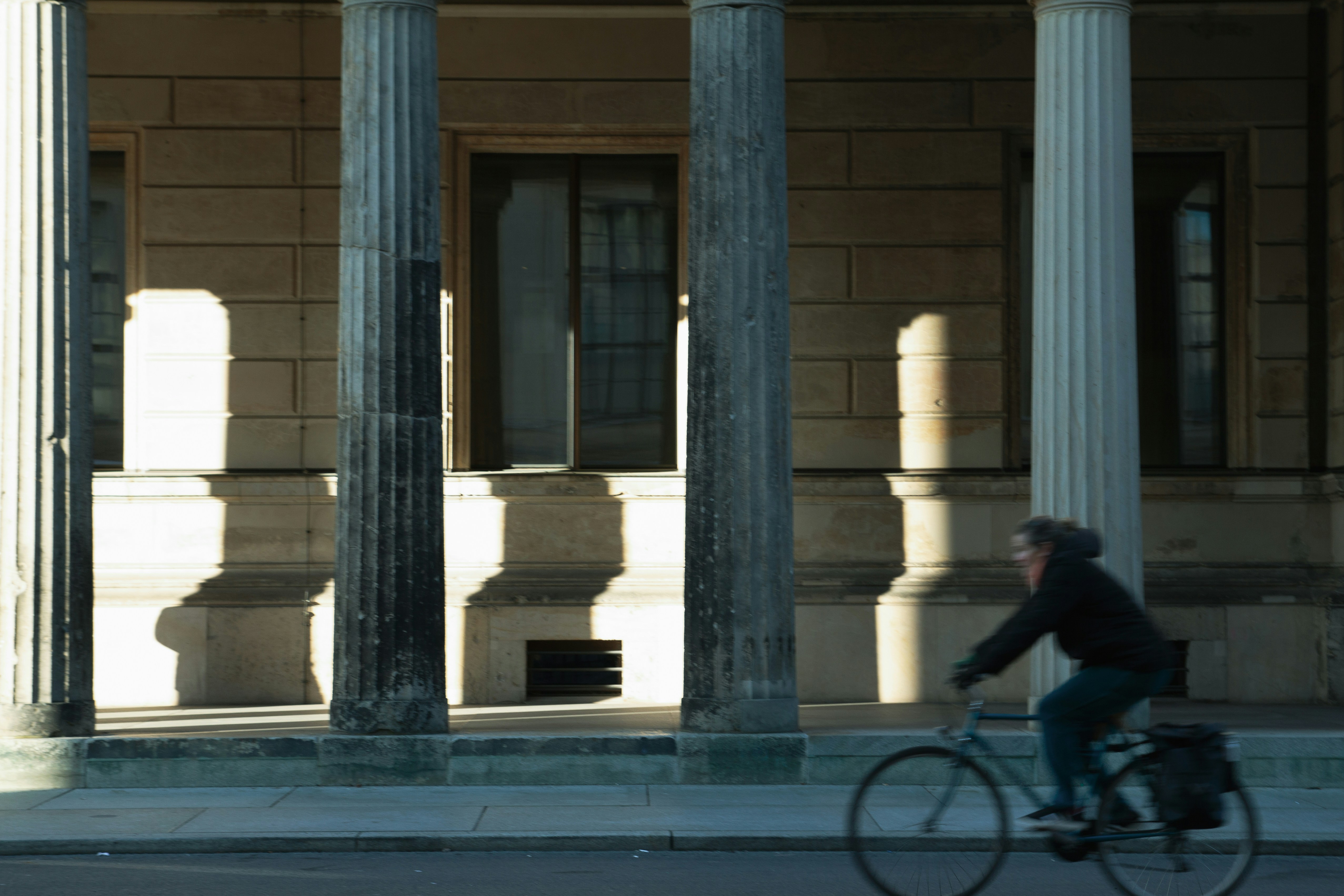 Motion in the Colonnade: Cyclist Passes a Quiet Classical Facade