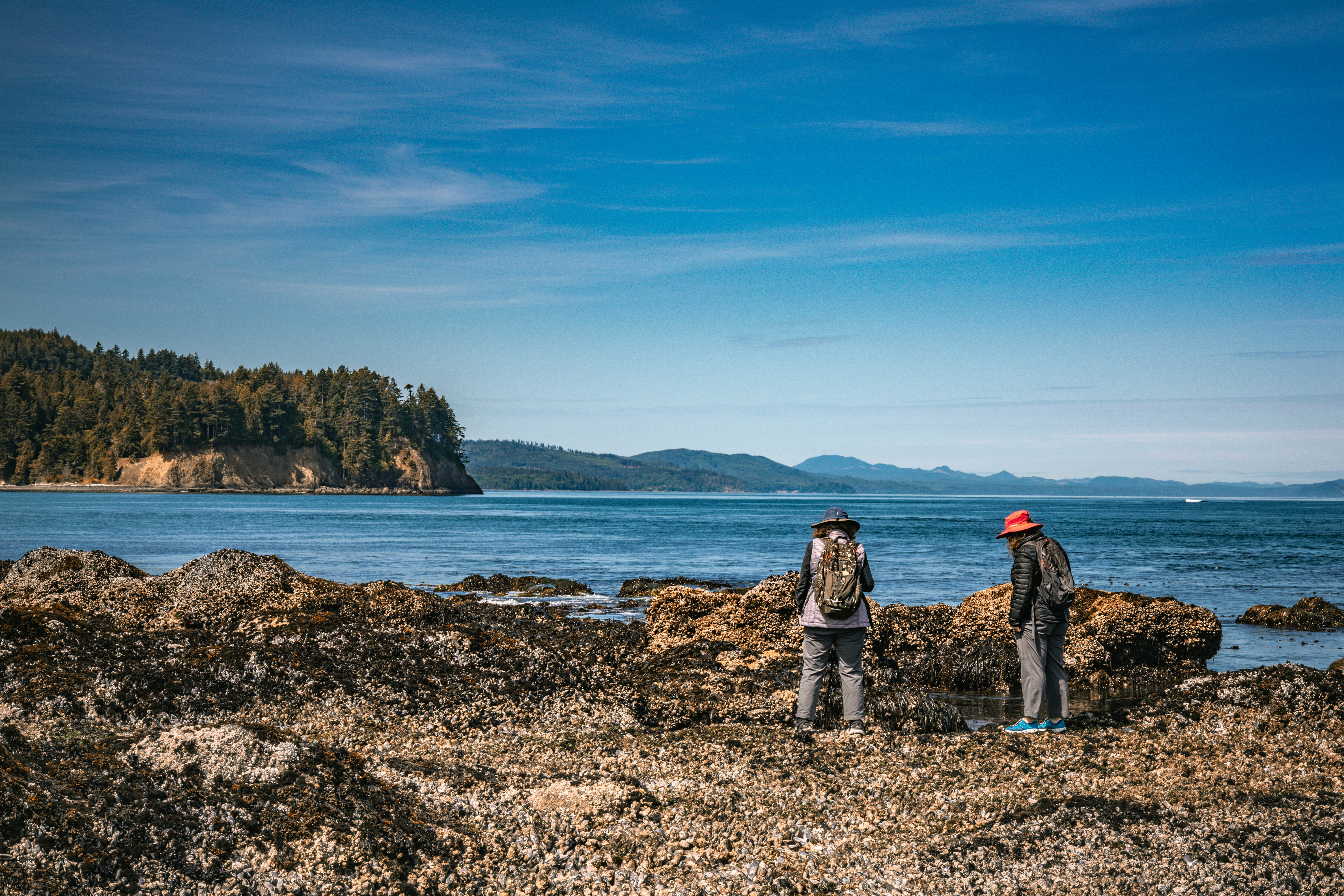 Two hikers at the rocky shore beneath a wide blue sky