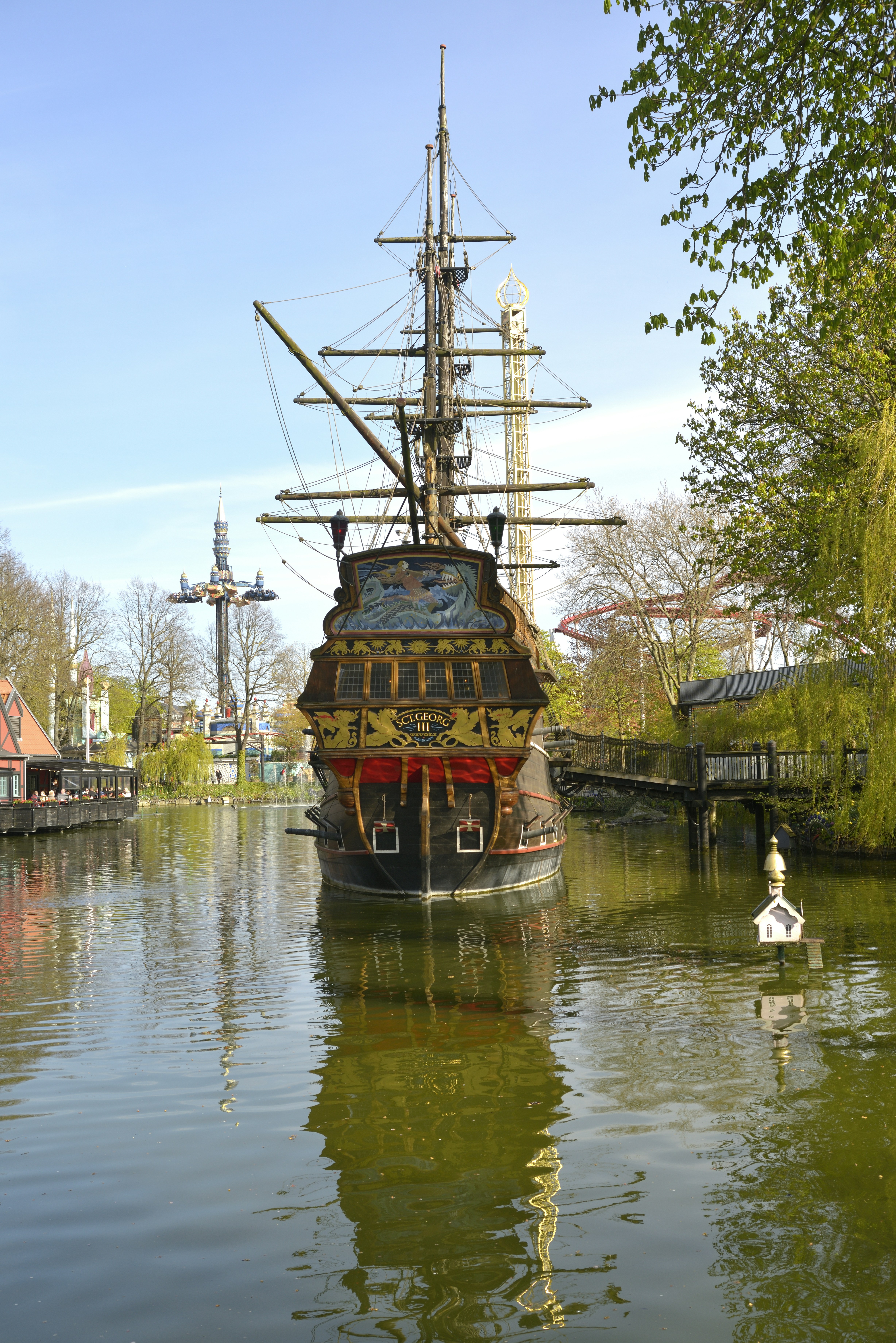 Tall Ship on Quiet Canal: A Historic Vessel Framed by a Sunny Riverside