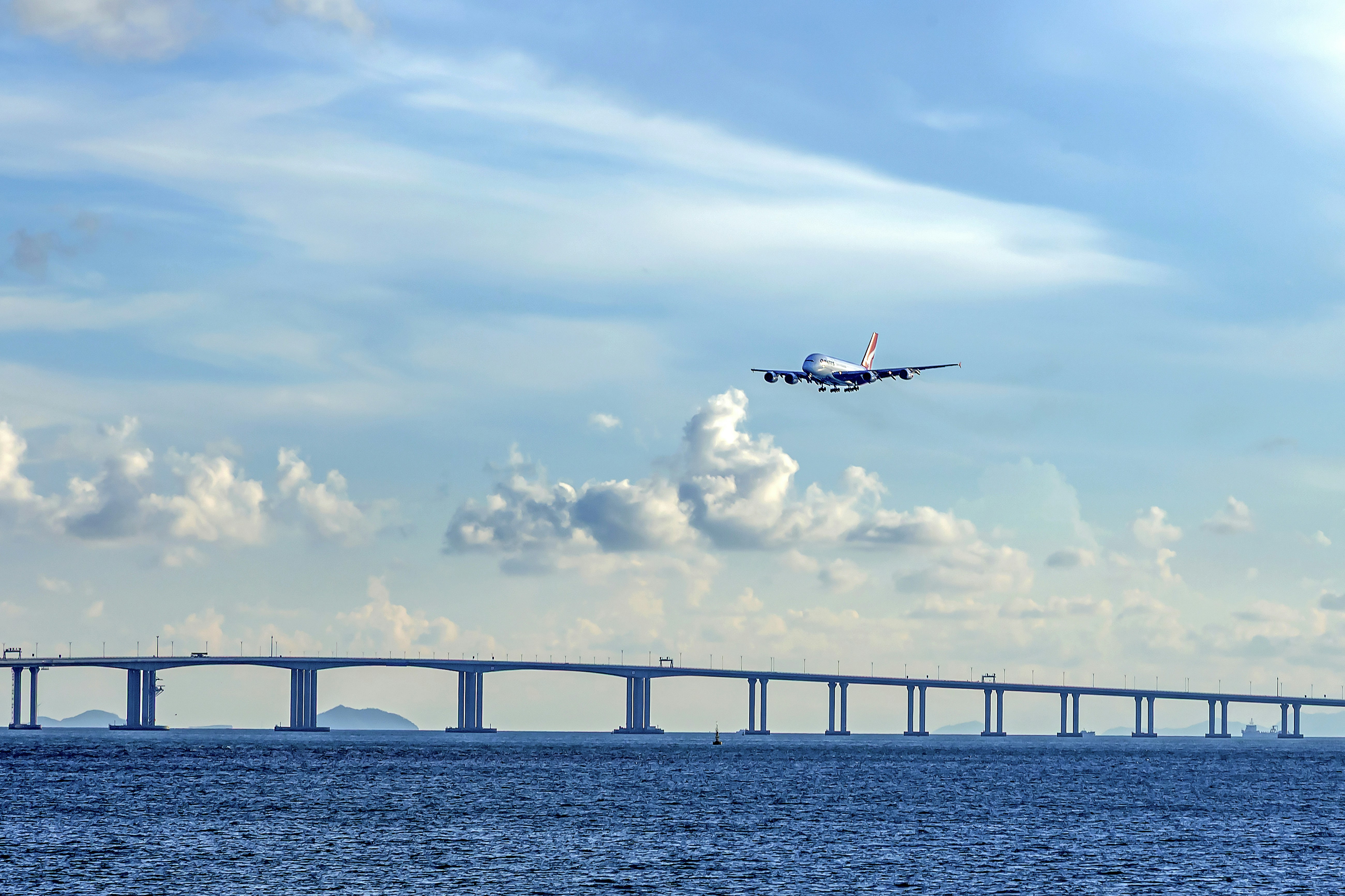 Airliner in flight over a sea-dotted bridge at horizon