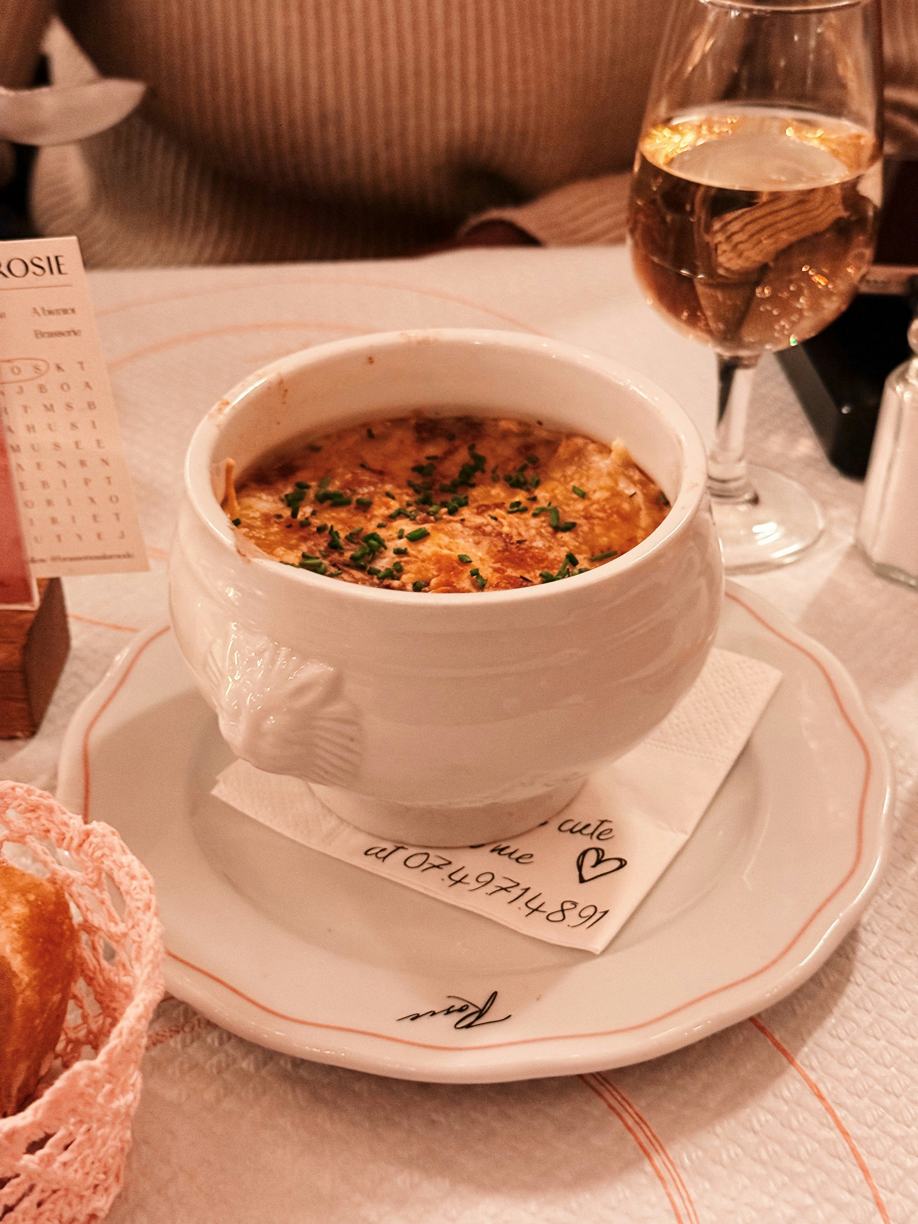 Creamy French Onion Soup in a White Lobed Bowl, Cornered by Glass and Table Setting