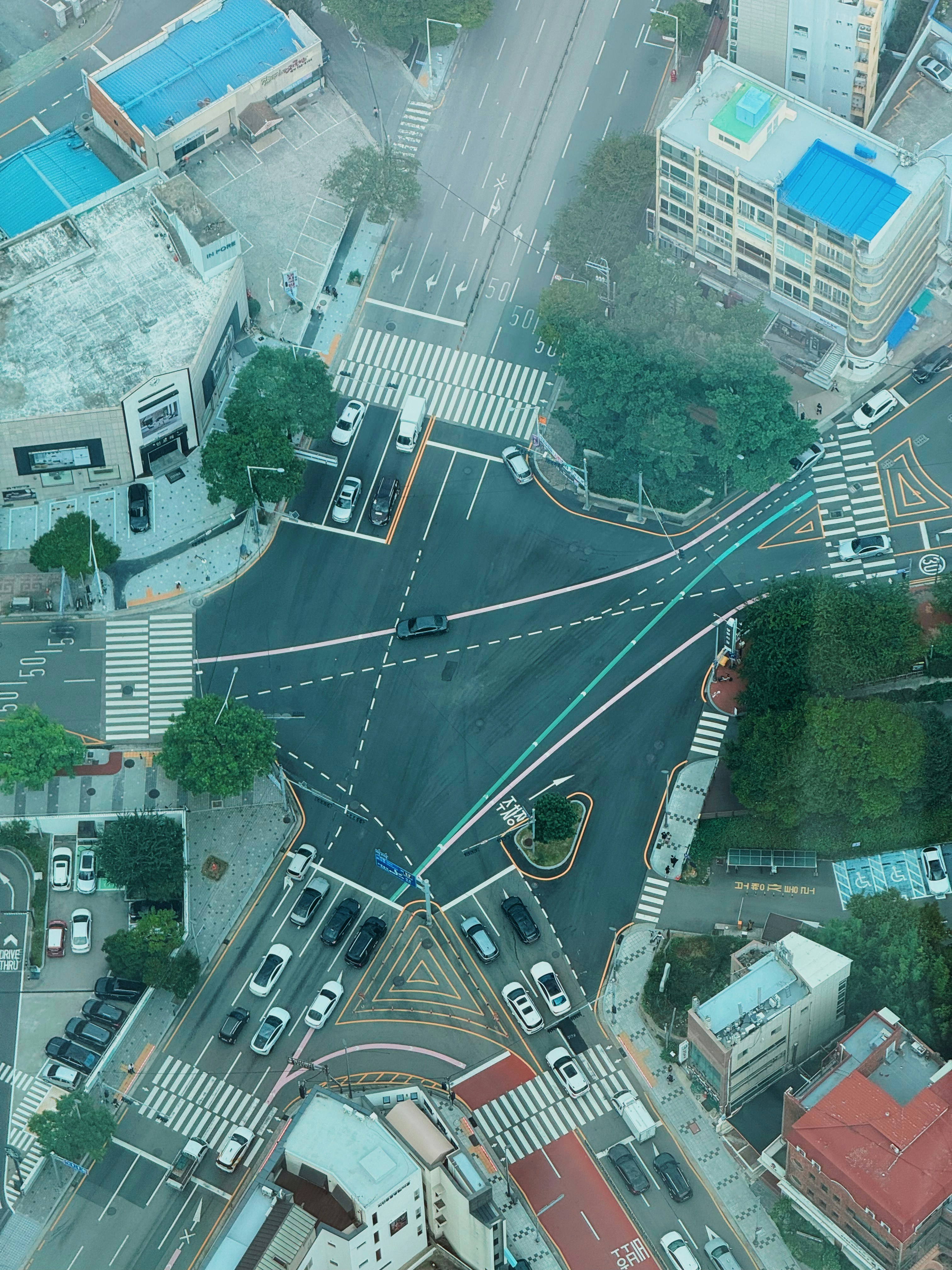 Bird's-eye view of a busy urban intersection with crosswalks, road markings, and surrounding buildings in a cool-toned morning light.