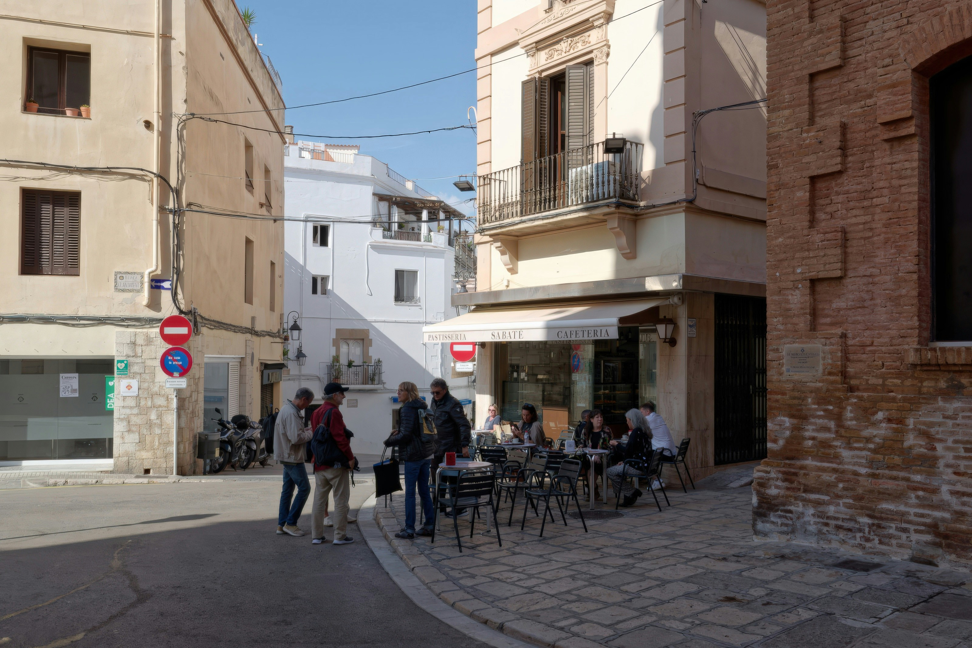 People sitting at outdoor cafe tables on a sunny street.