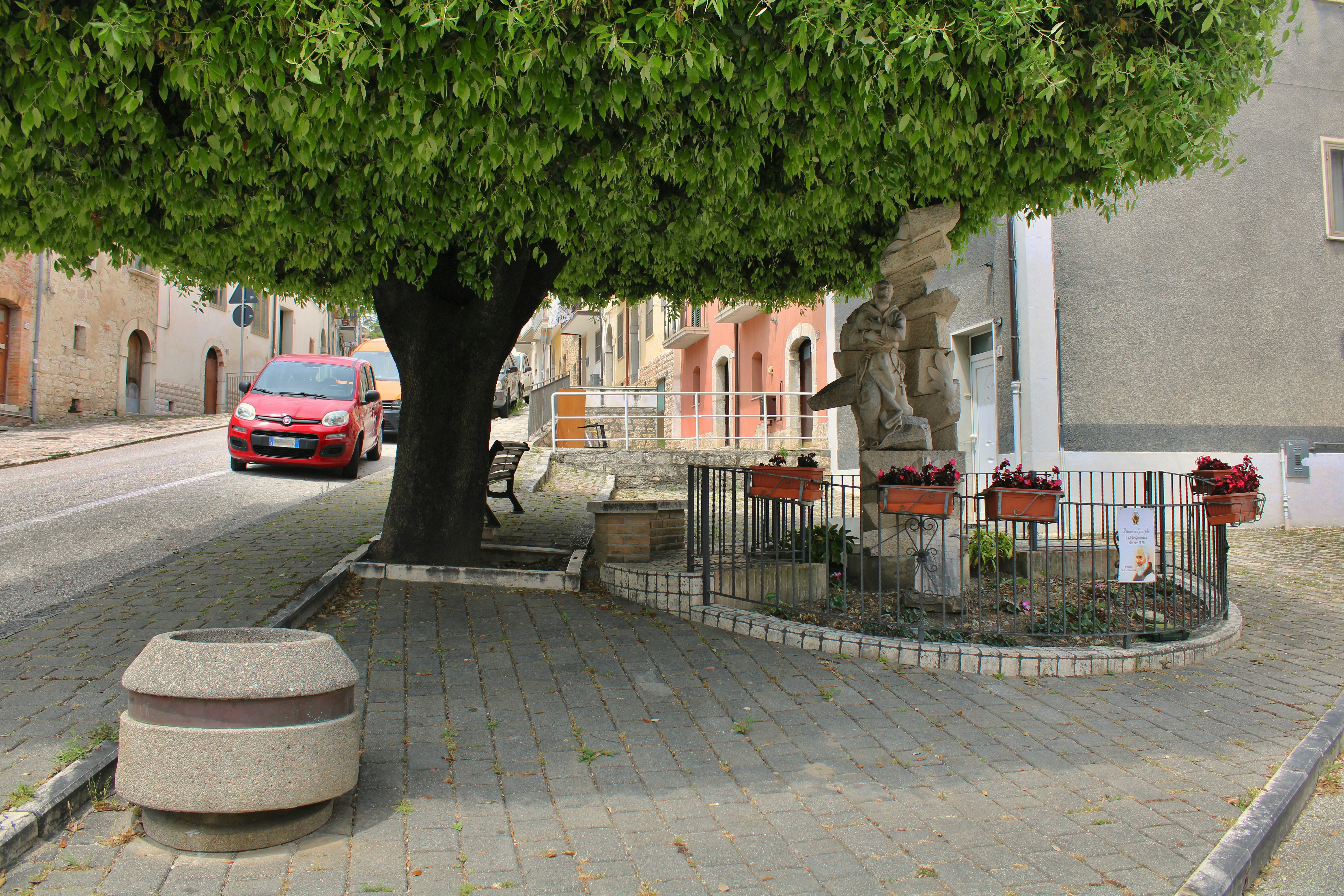 Sunlit Town Square with Red Car and Statue Garden