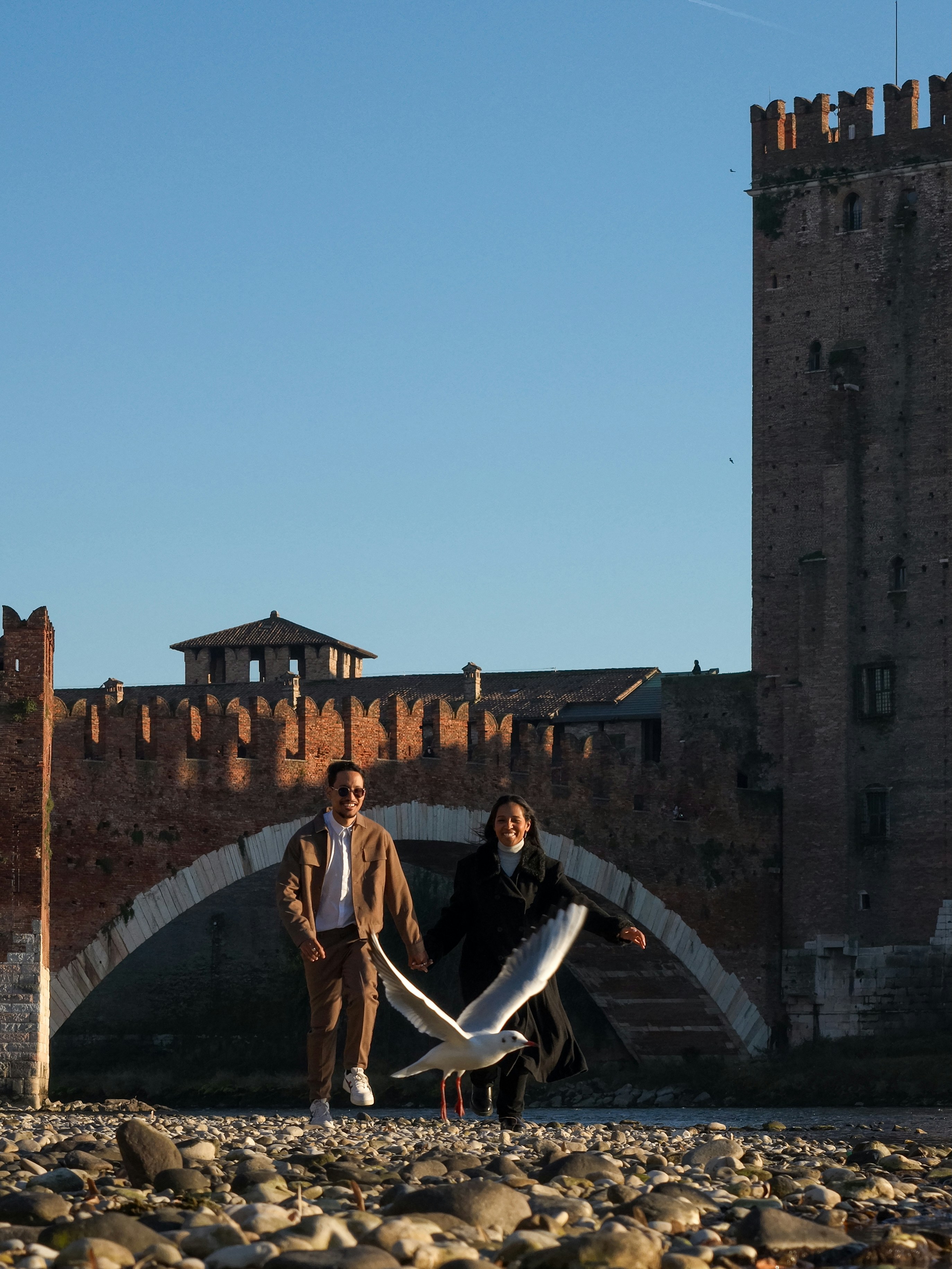 Two Travelers and a Seagull Under a Medieval Bridge