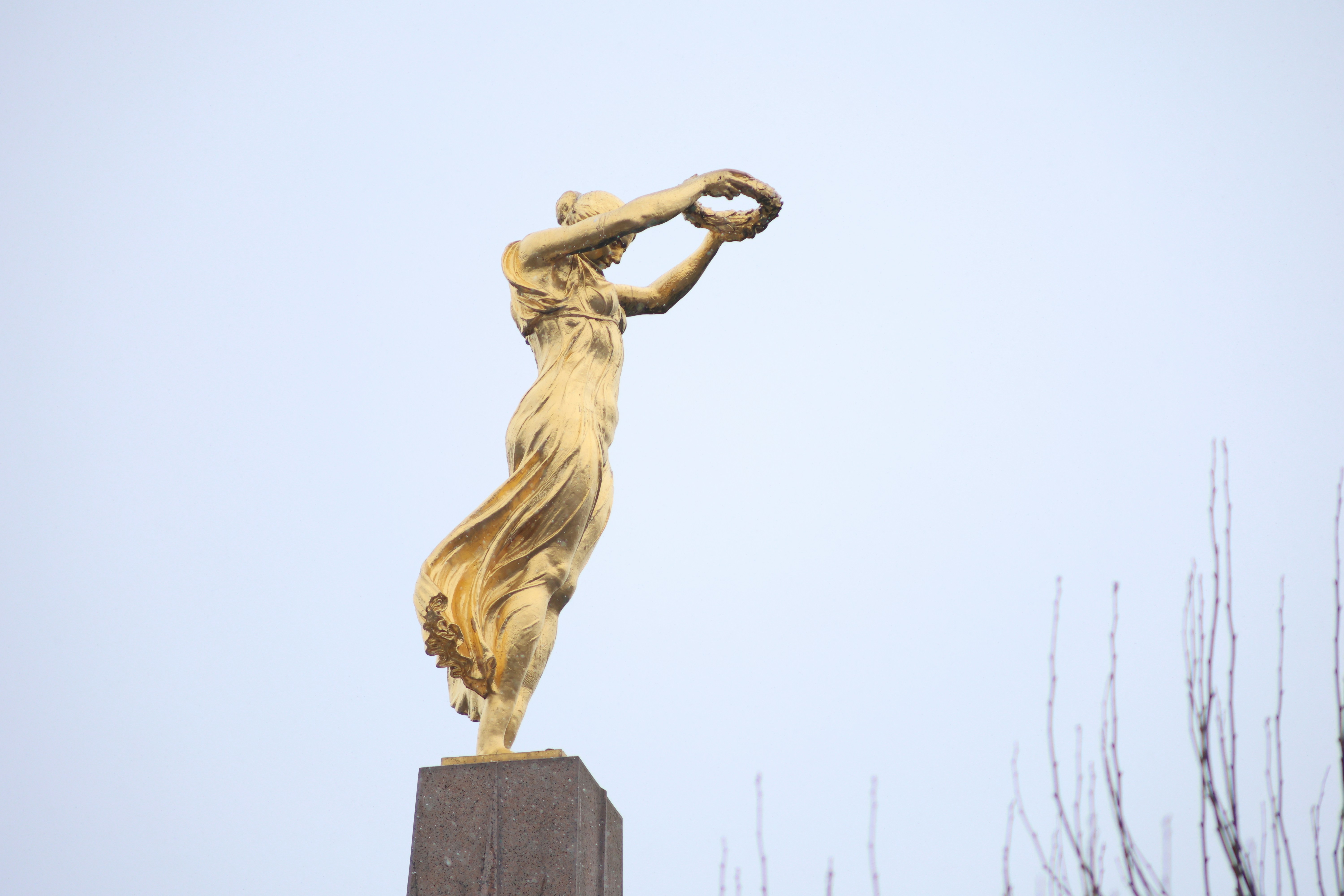 Golden Sail of Stone: A statue poised against a pale sky