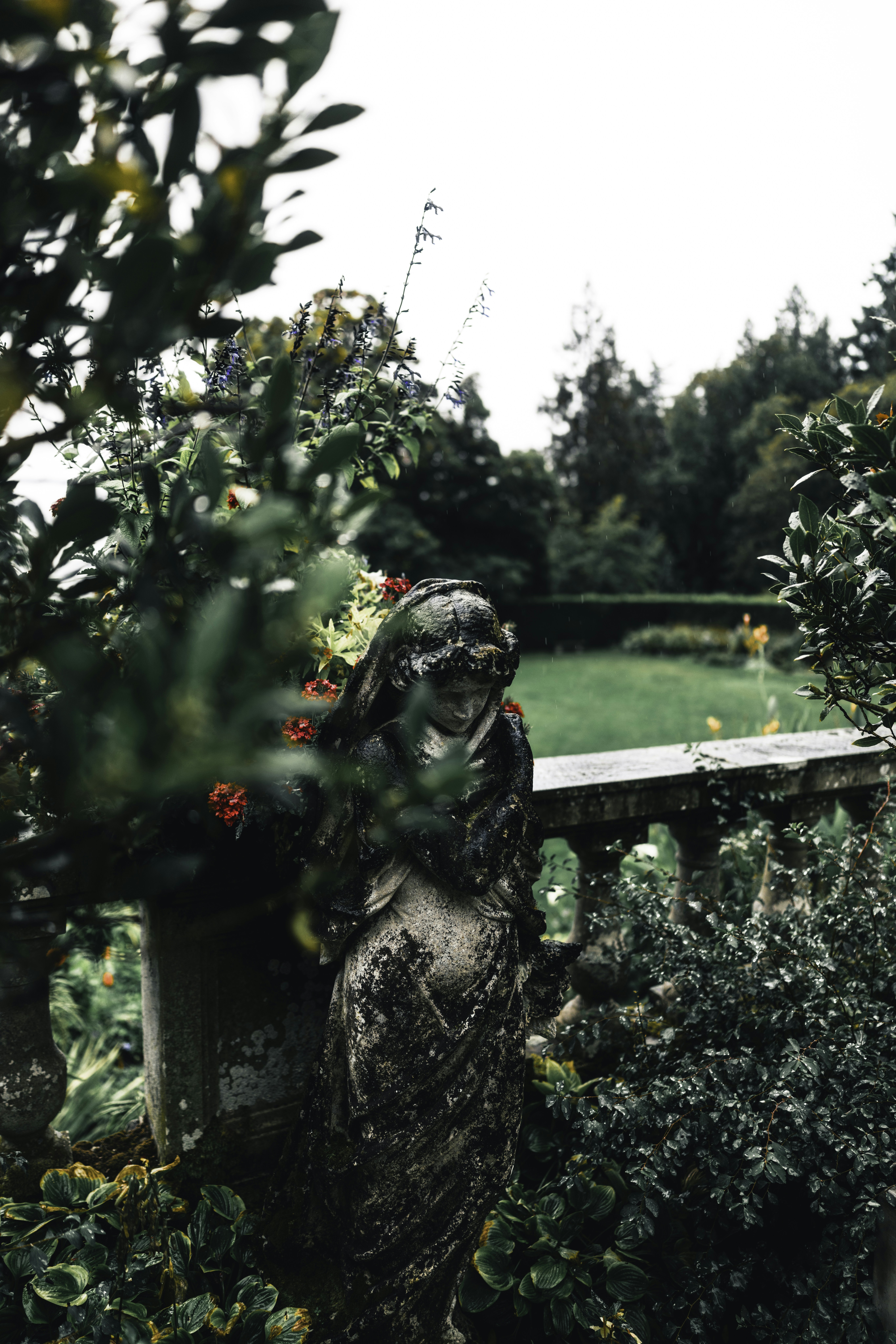 Weathered statue in a mossy garden rots among flowers and ivy