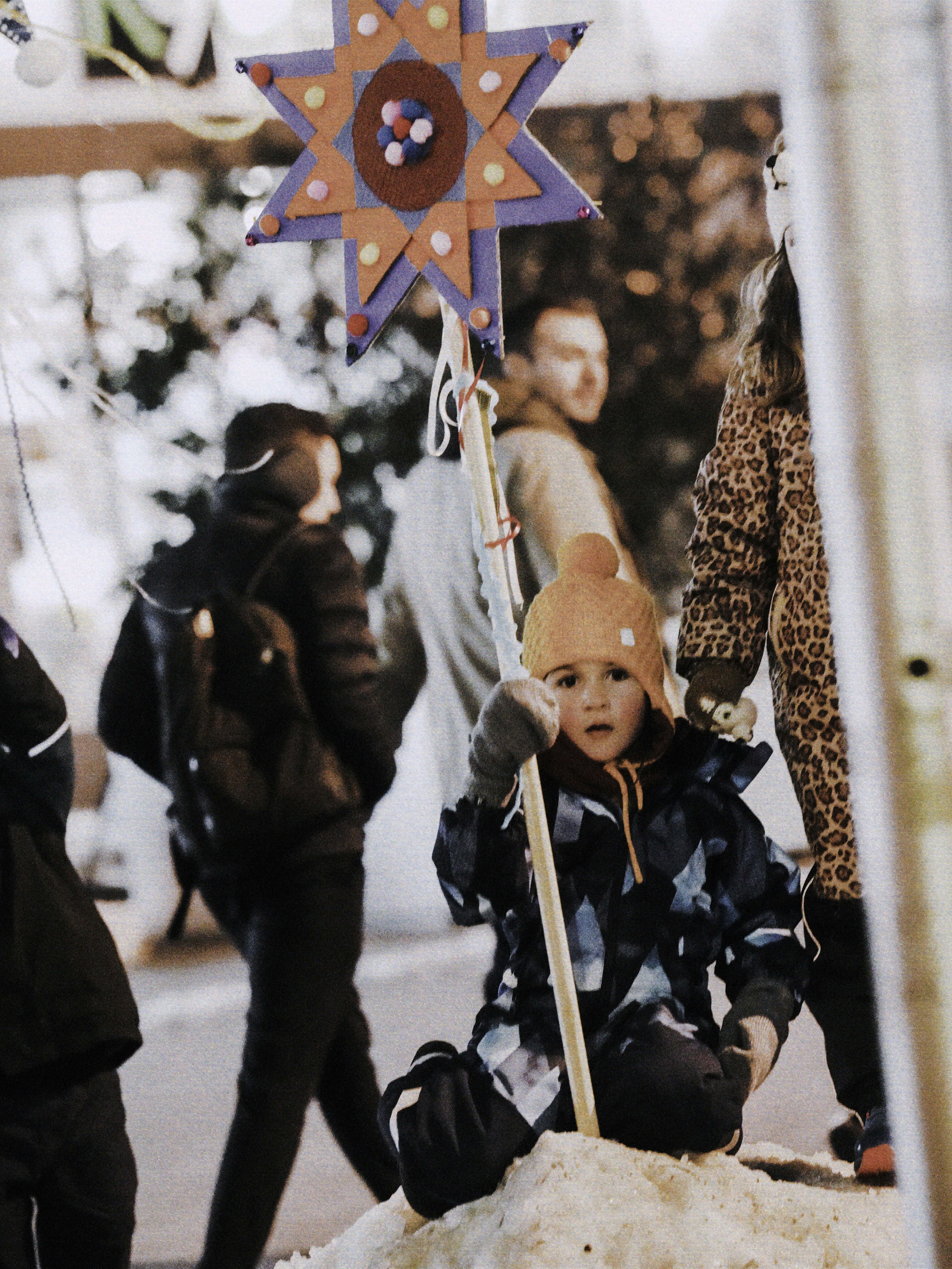 Child with orange hat holds star lantern at a holiday market