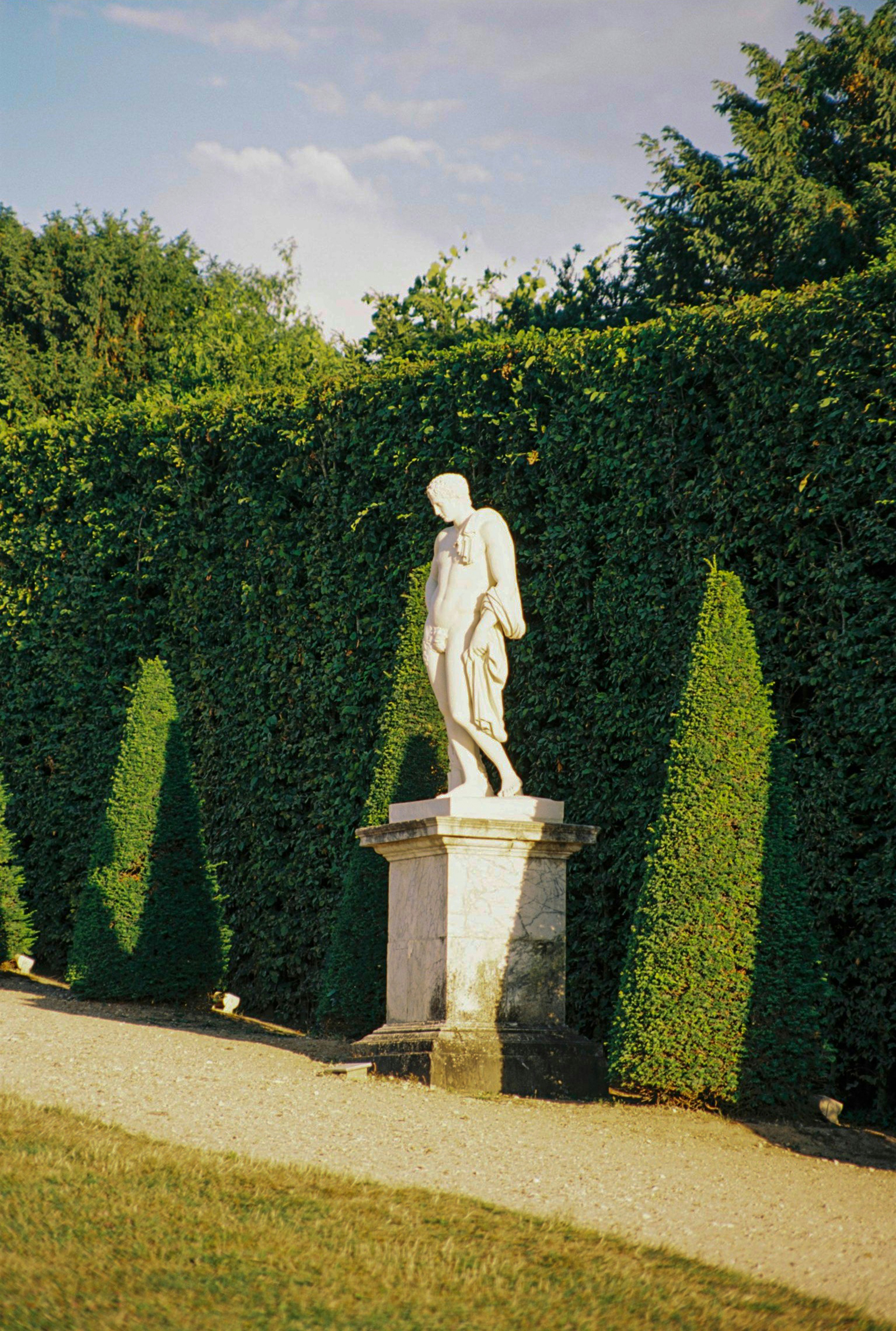A marble statue stands in a garden with manicured hedges. photo – Free ...