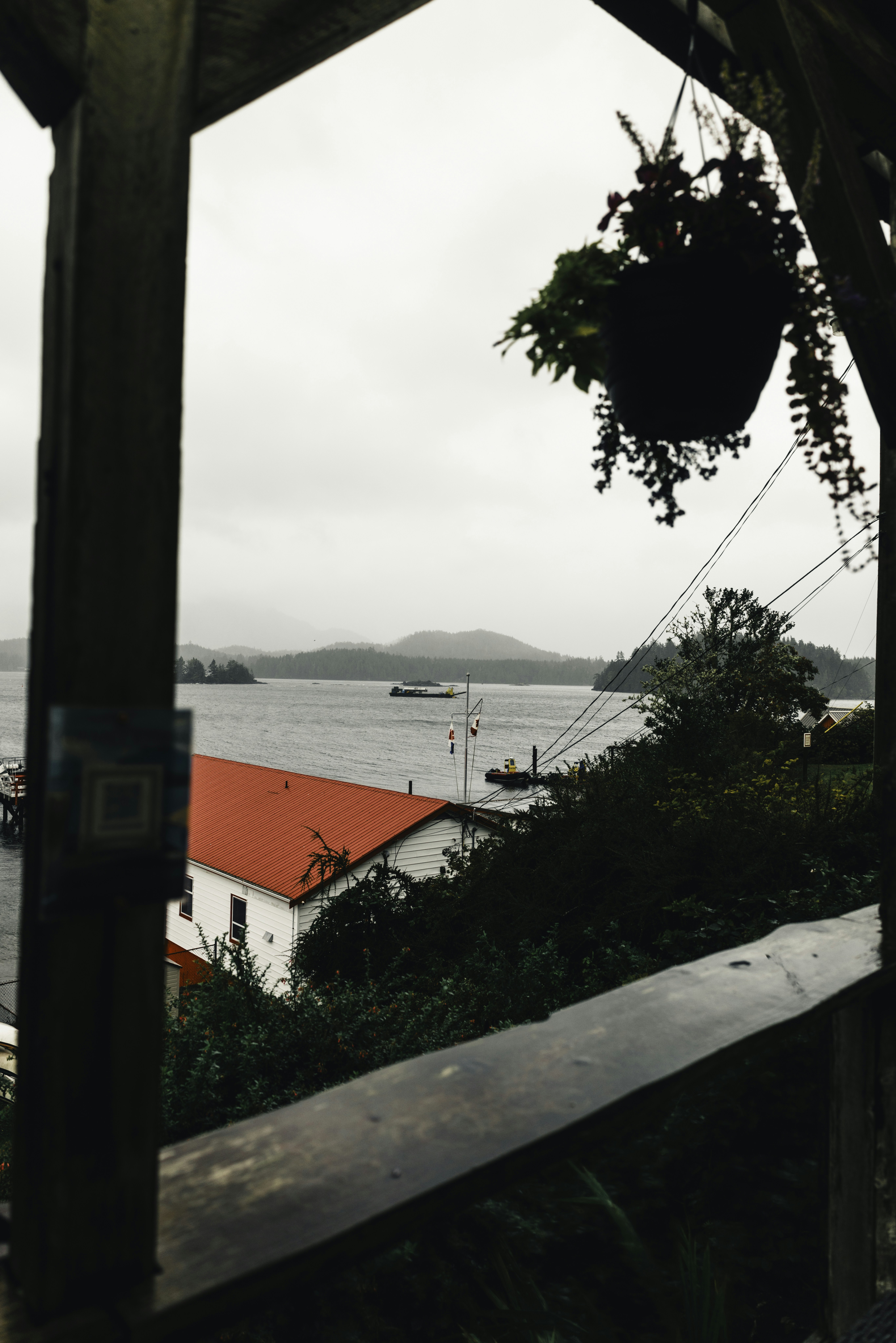 Red-roofed boathouse by a misty harbor framed by a rustic balcony