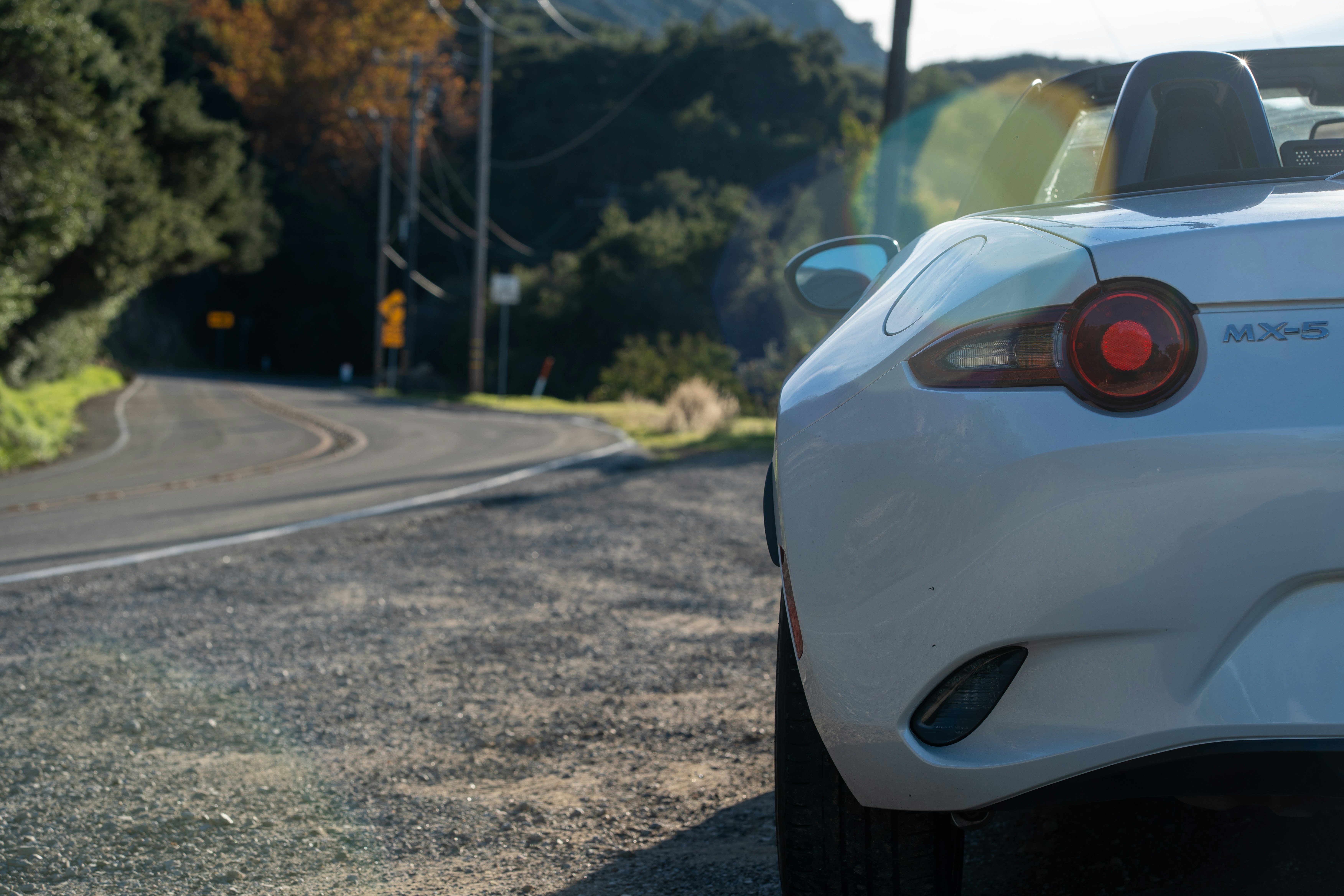 Rear-view of a white sports car resting on a sunlit roadside