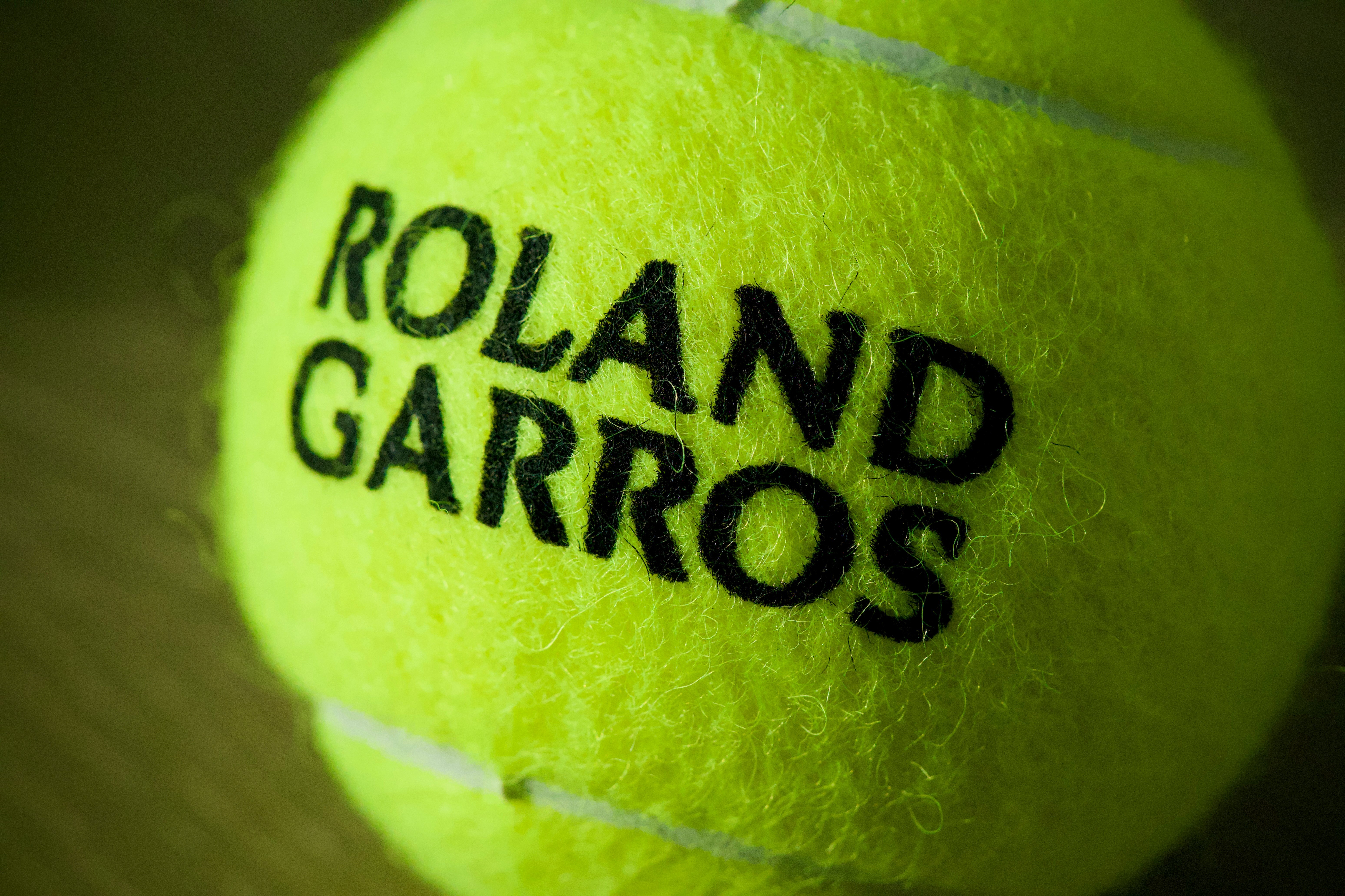 Close-up of a Roland Garros tennis ball: neon fuzz and stitched crease